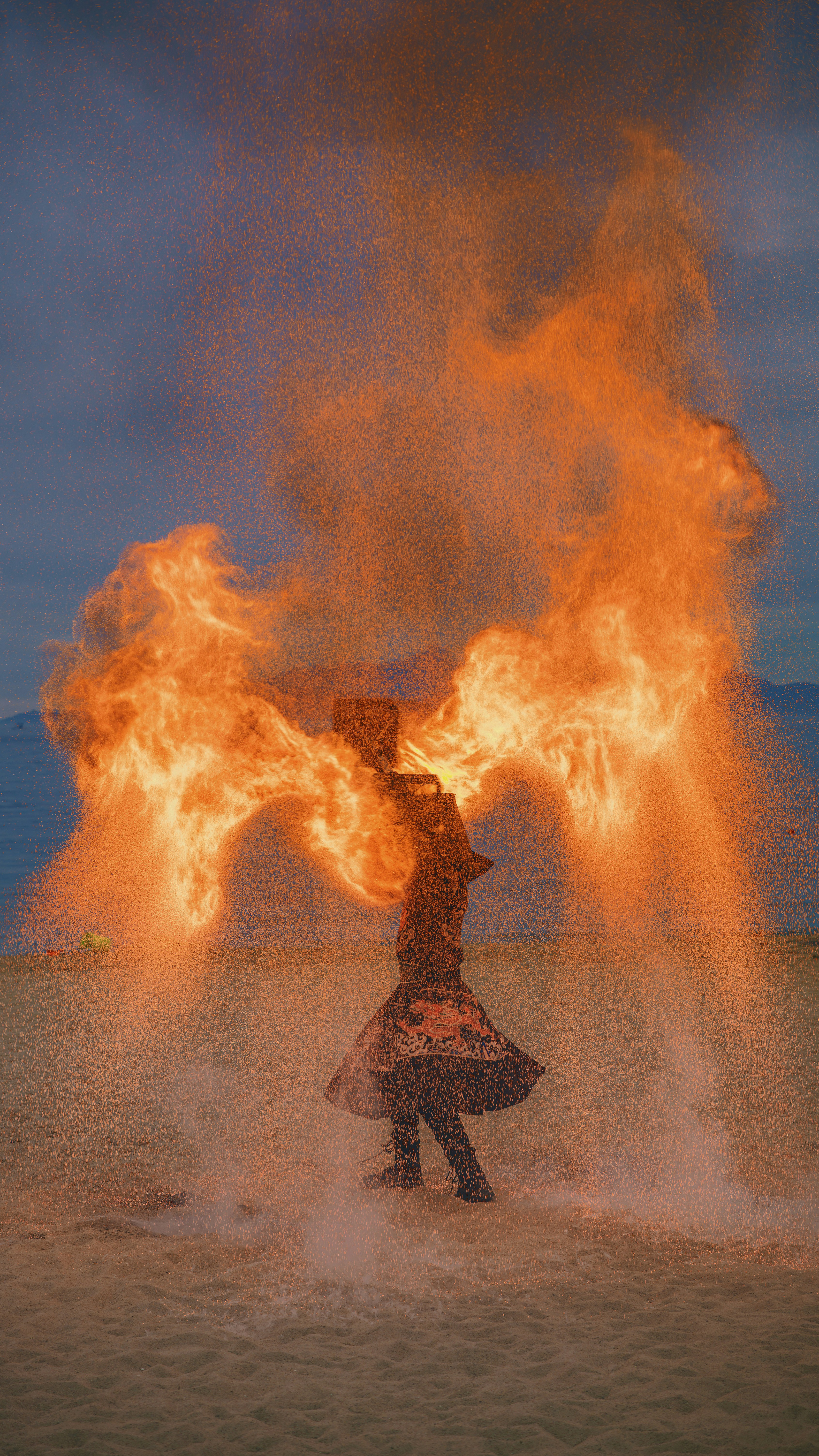 Fiery Silhouette: A Dancer Conjures Twin Flames on a Windy Beach at Dusk