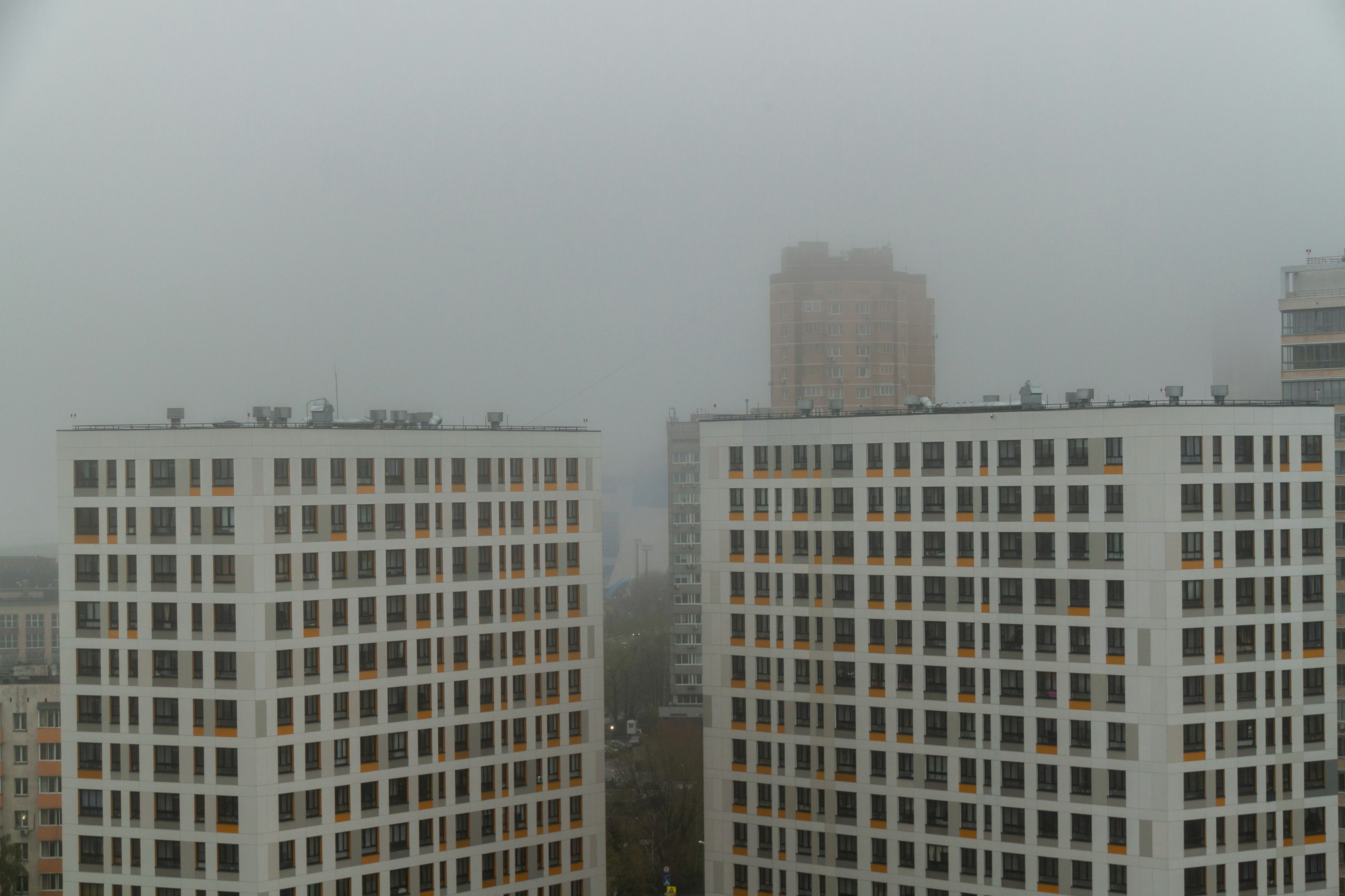 Foggy urban skyline with two white and orange high-rise buildings in soft light.