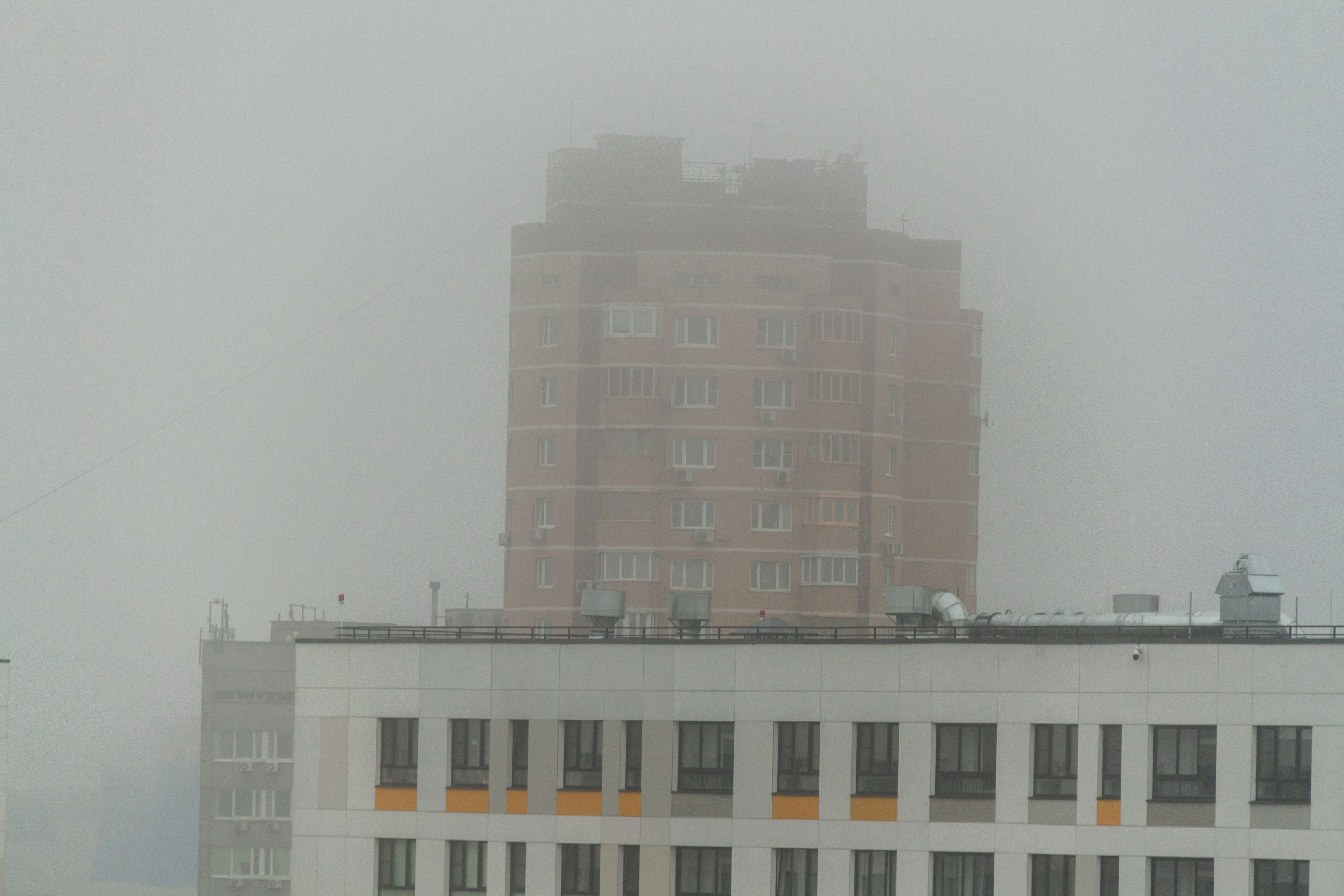 Muted high-rise silhouette enveloped in dense fog, creating a serene urban scene with diffused pastel tones.