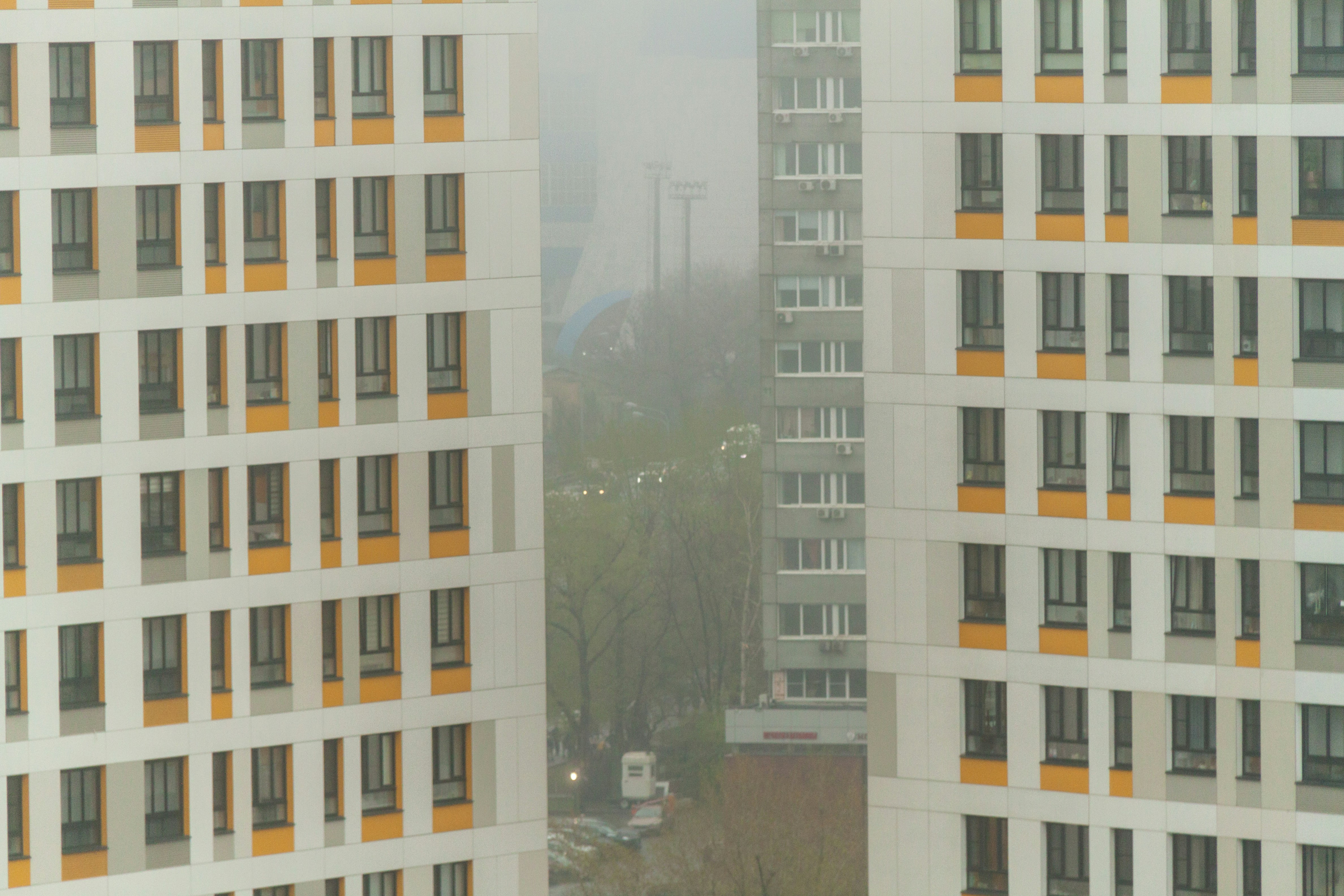 Two high-rise buildings with orange and white panels frame a misty cityscape, softening the geometric lines.