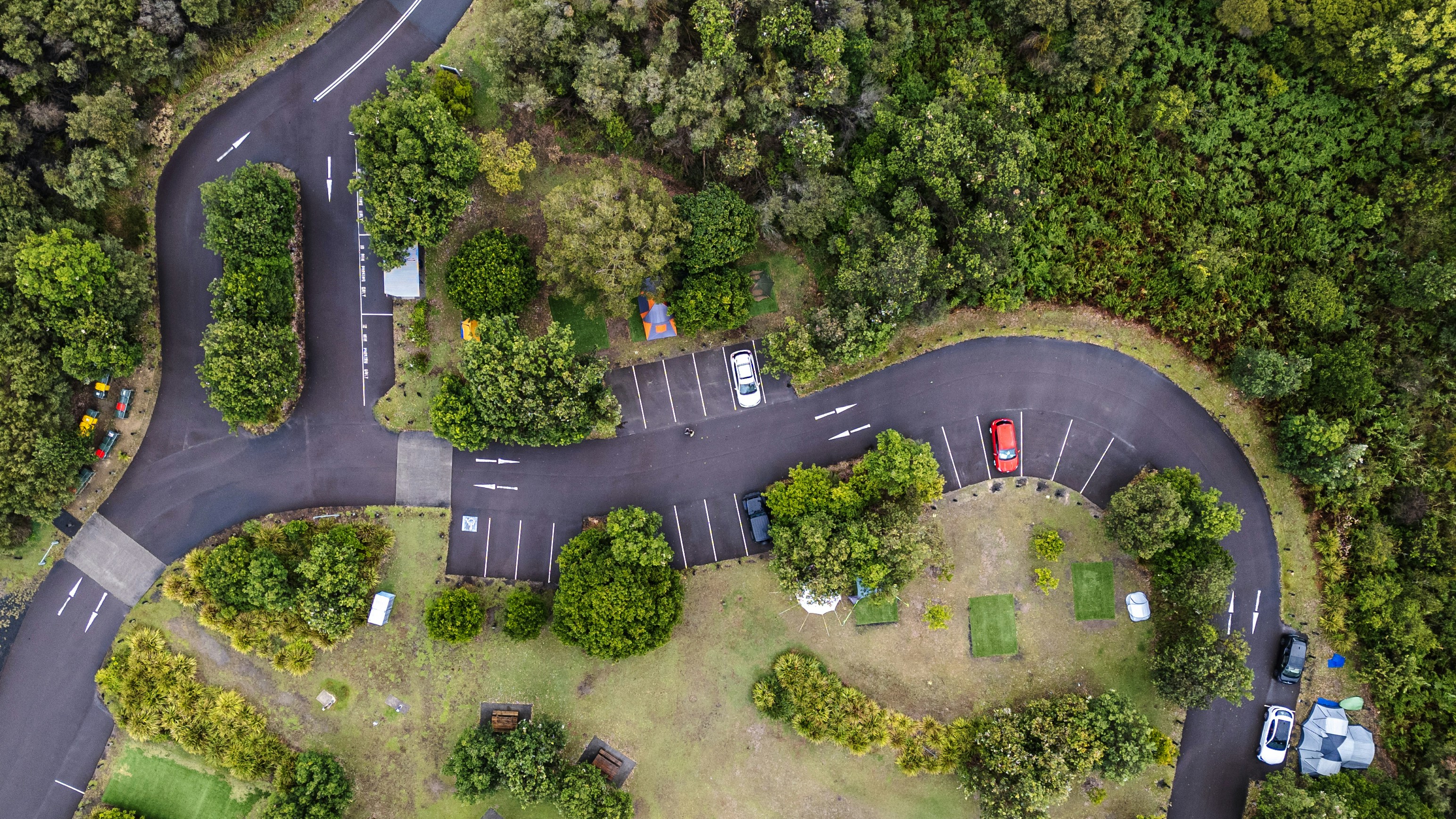 Aerial view of a parking area seamlessly integrated into lush greenery, with vibrant tents and vehicles adding colorful accents.