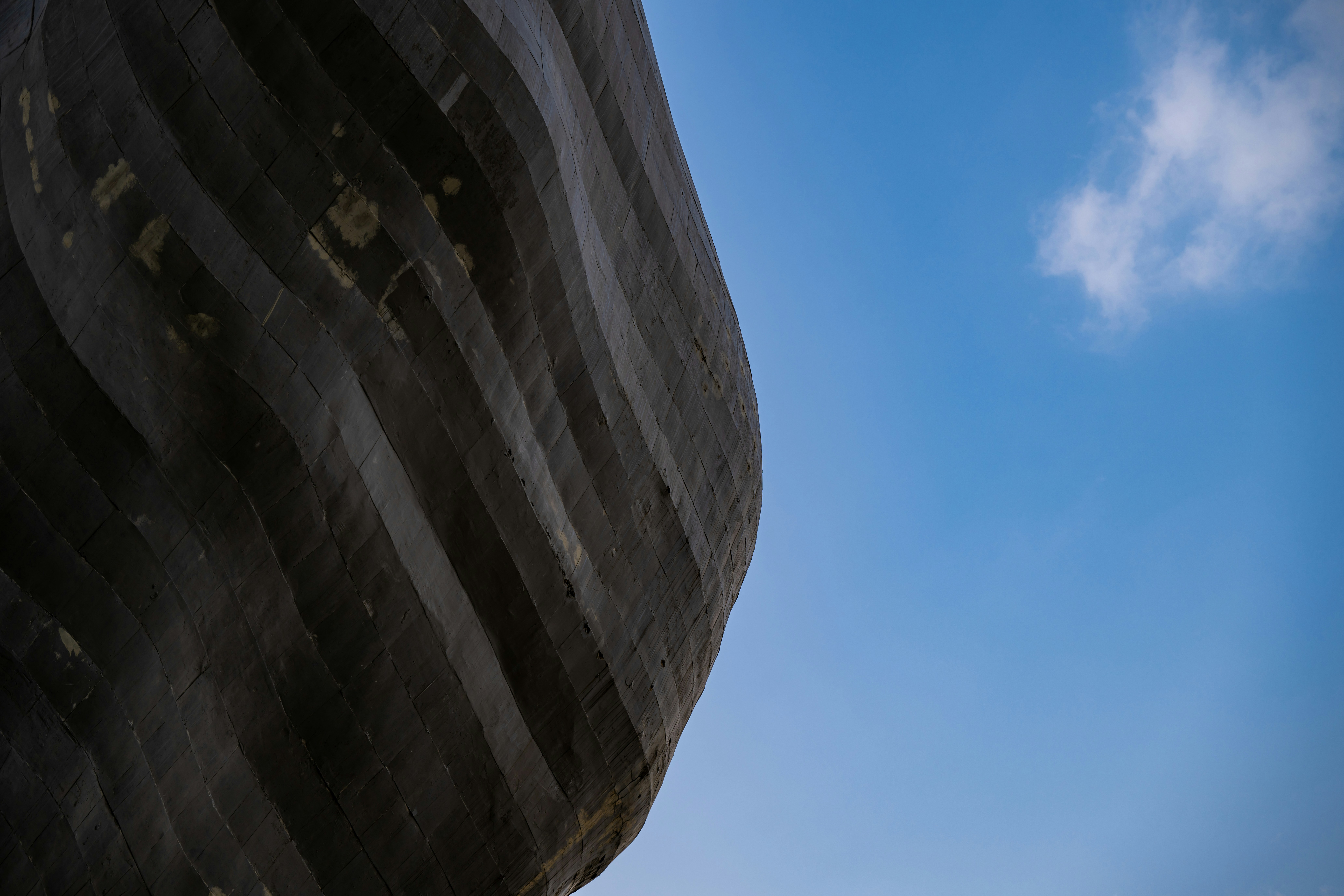 Curved, textured stone structure set against a clear blue sky.