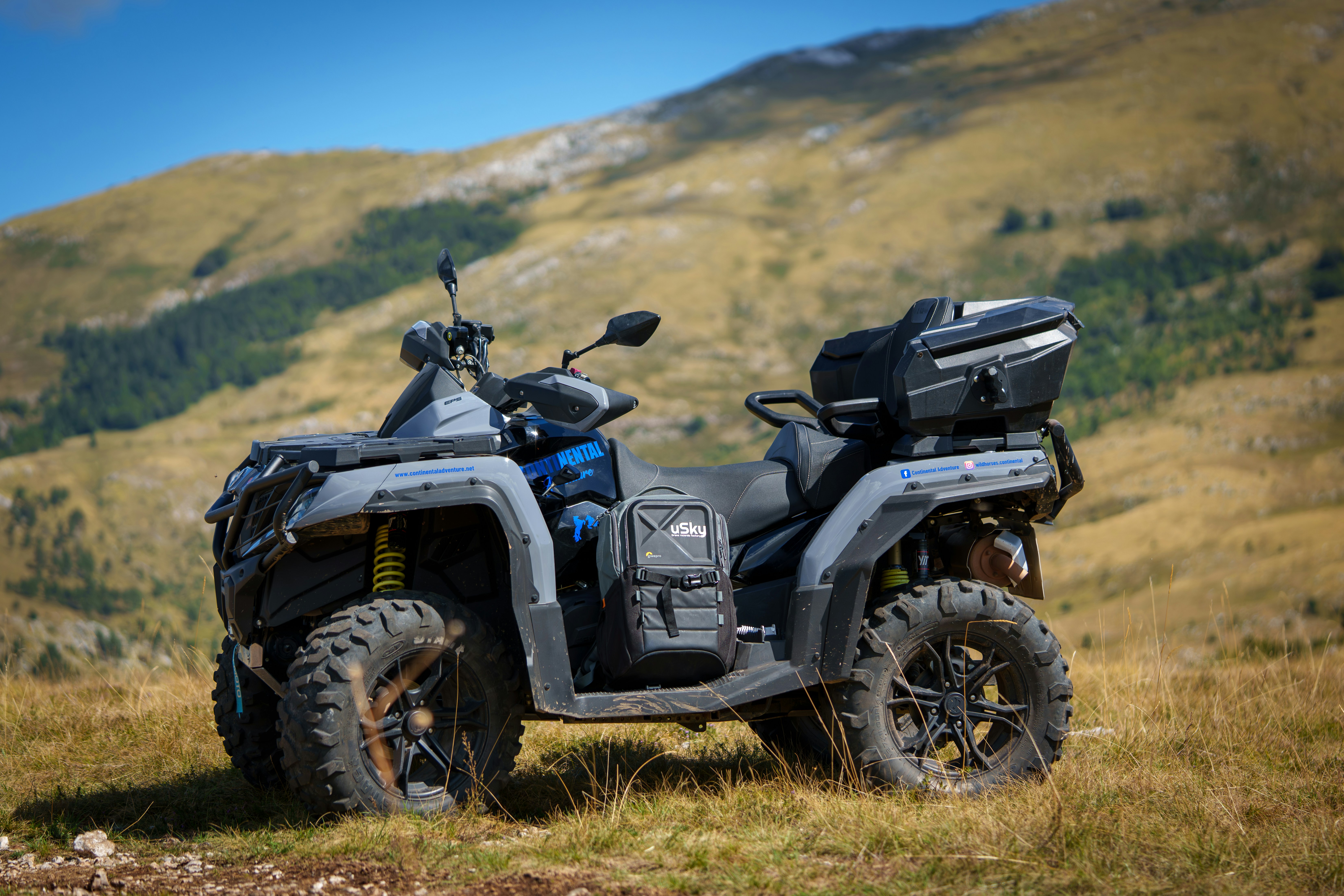 A four - wheeler parked in a field with mountains in the background ...