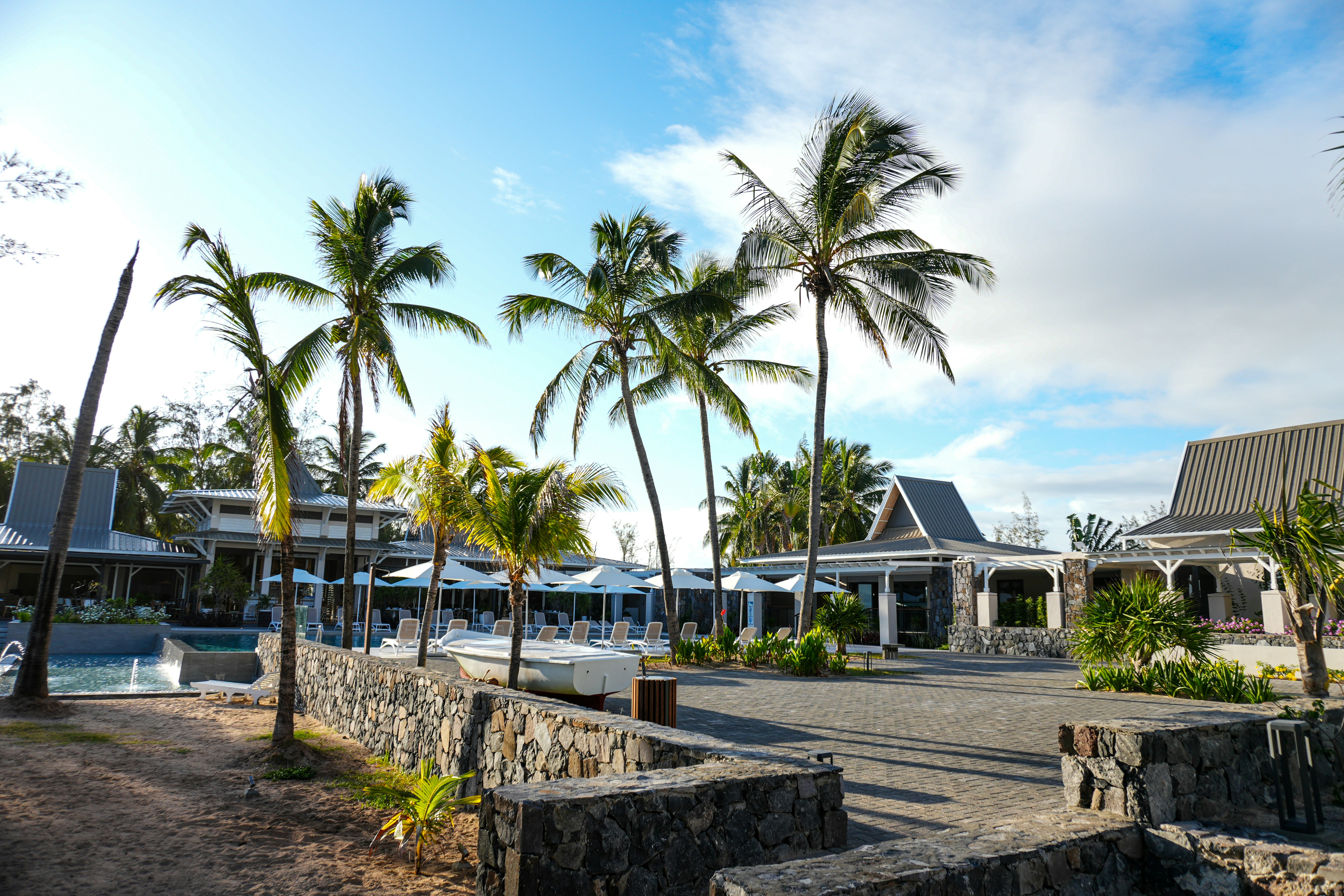 Palm trees sway above a tranquil resort pool area with stone walls and sunlit buildings.