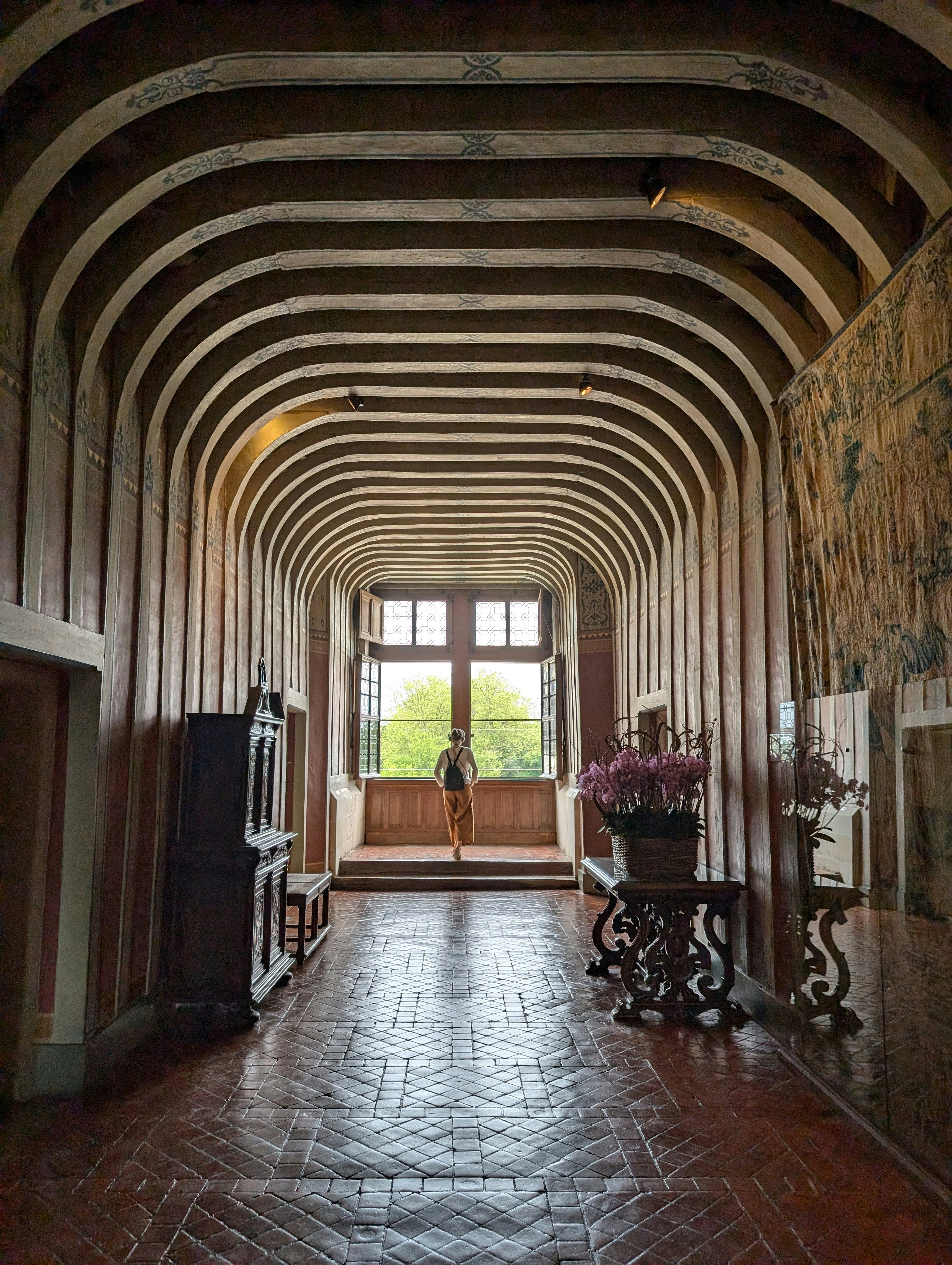Long vaulted corridor with repeating arches leads to a sunlit window. A lone figure stands at the far end, bathed in warm light.