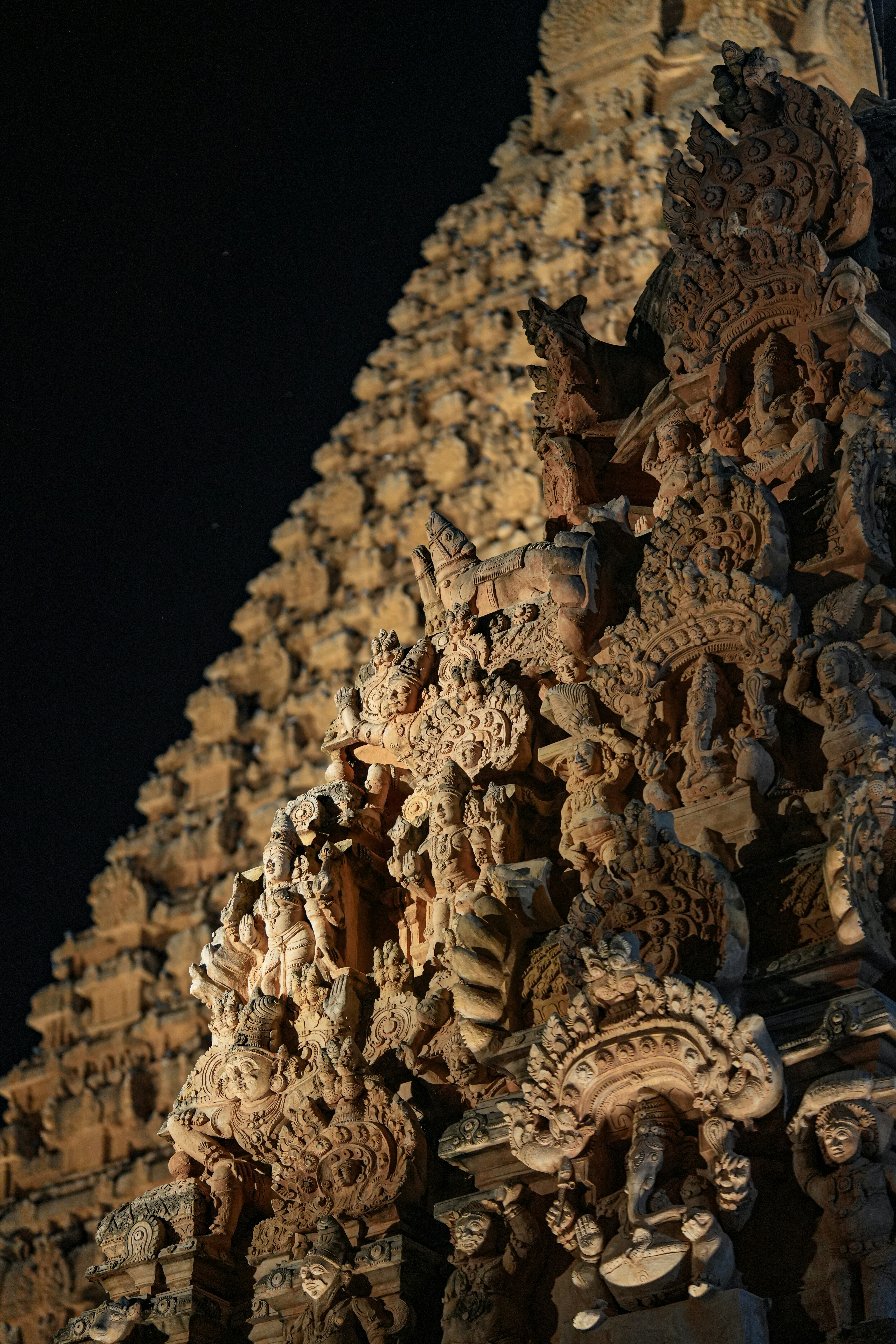 Intricate carvings of deities and mythical figures adorn the temple facade, illuminated by soft light against the night sky.