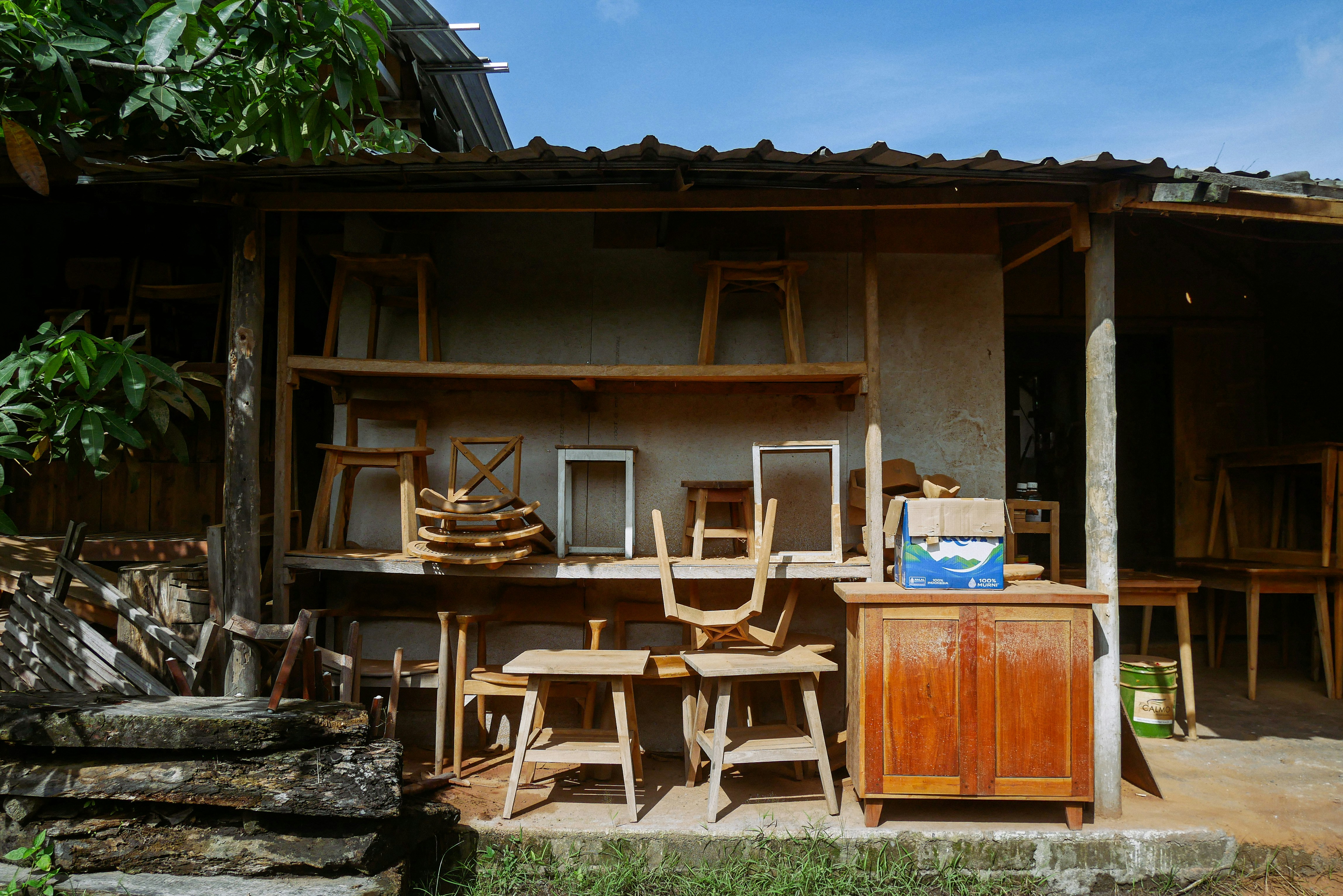 Wooden chairs and stools arranged in a sunlit outdoor workshop.