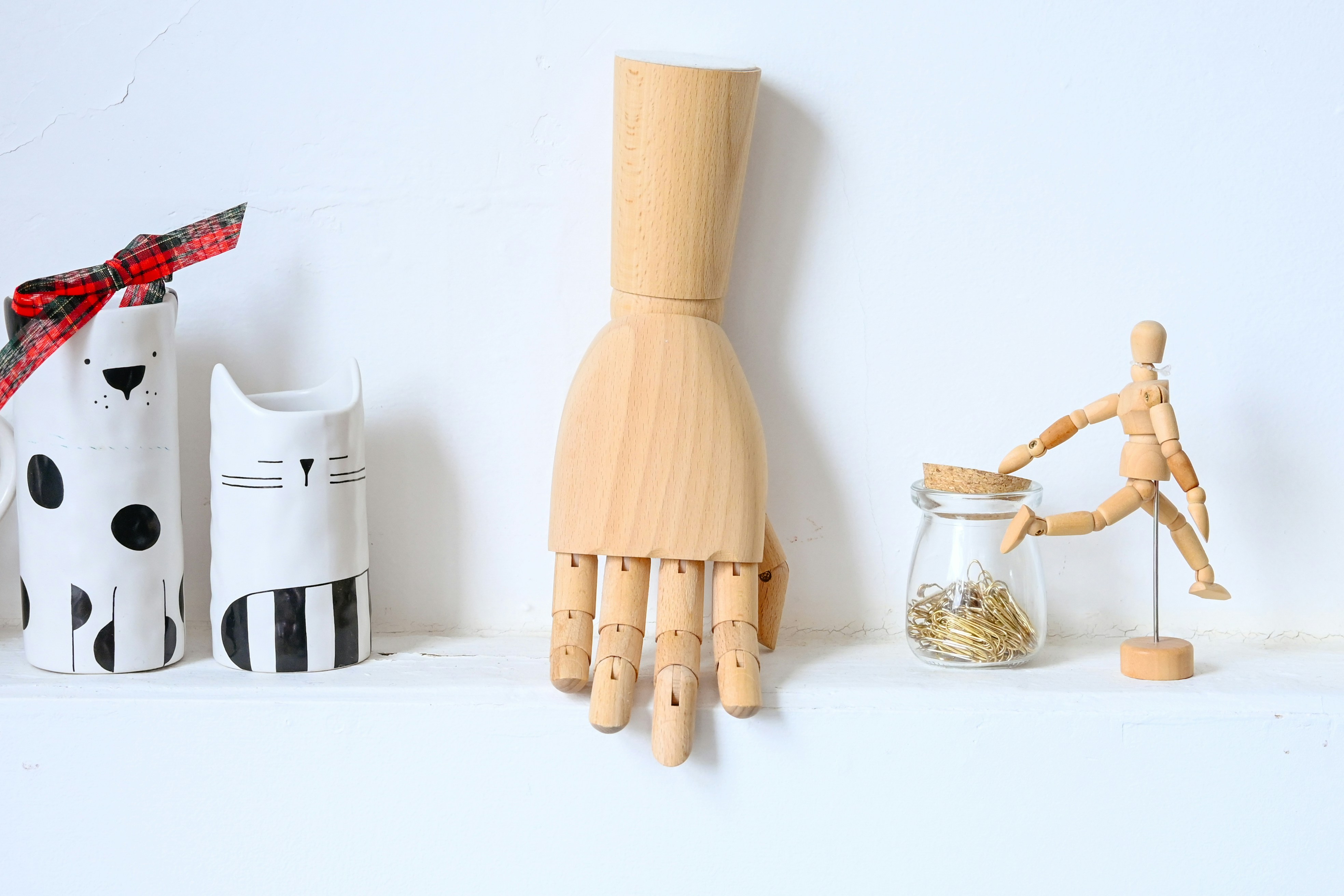 Wooden hand and mannequin alongside ceramic cat containers on a white shelf.