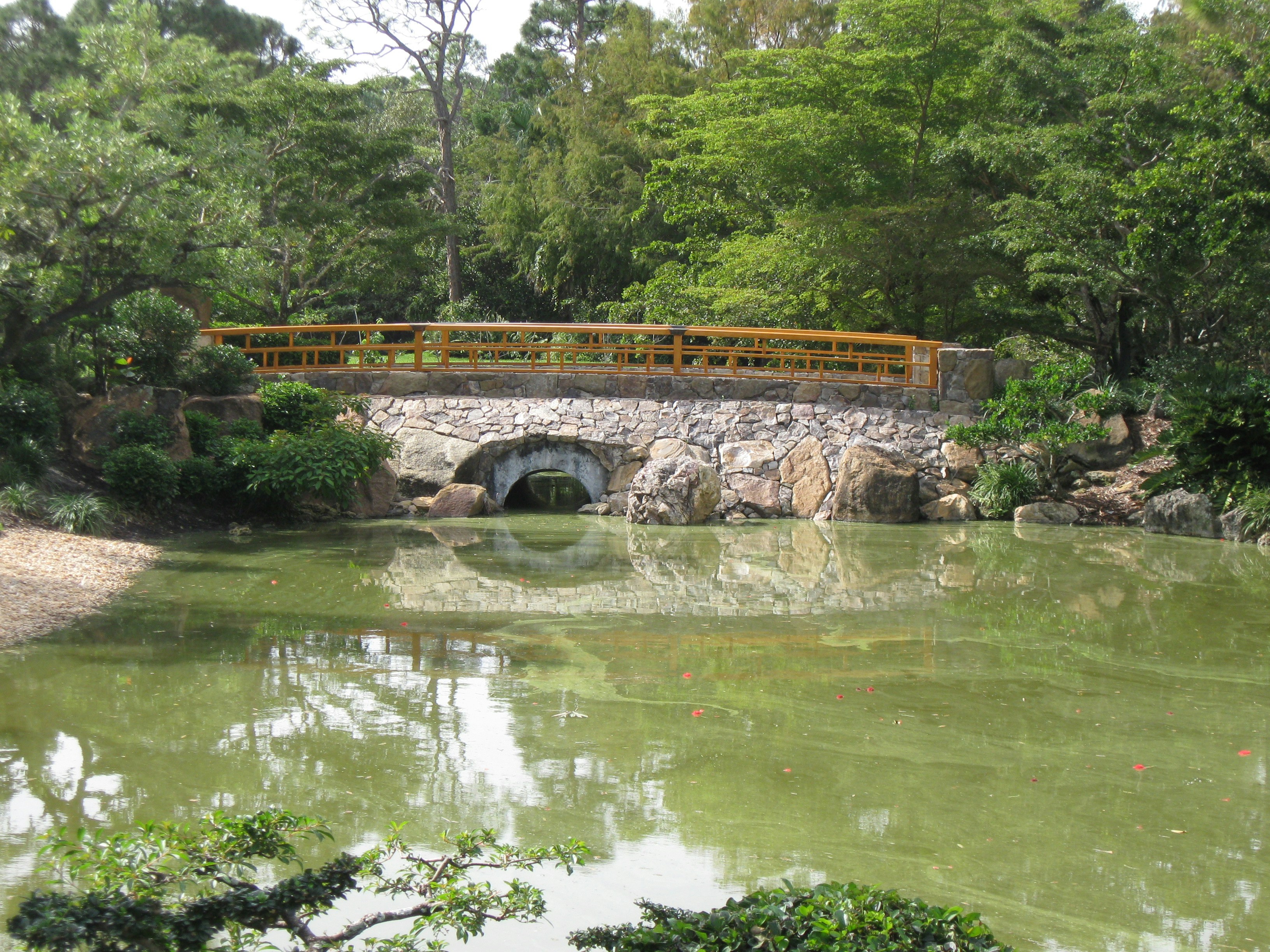 Stone bridge arches over a reflective pond surrounded by lush greenery.