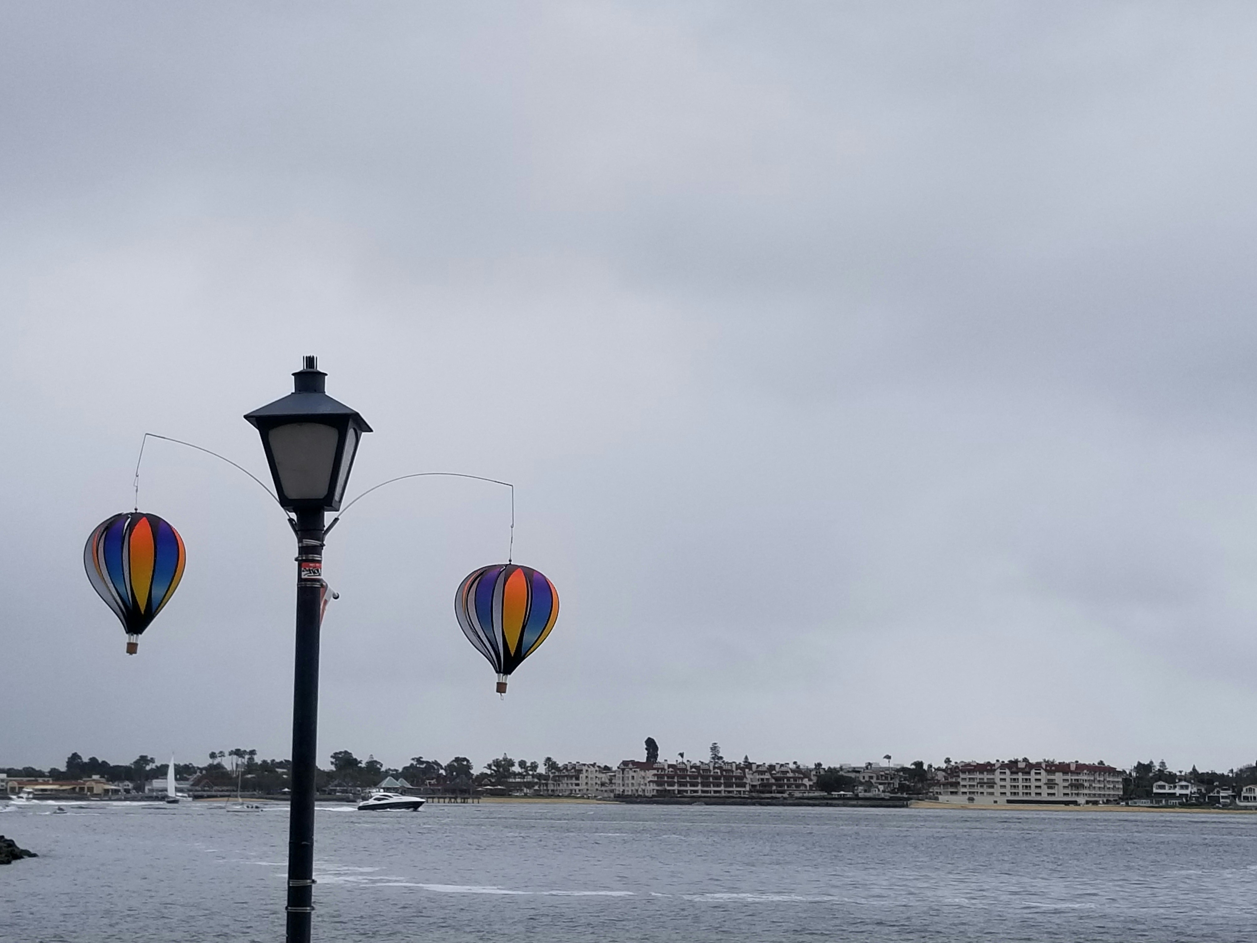 Twin Balloons Over a Calm Coastal Scene Under Gray Skies