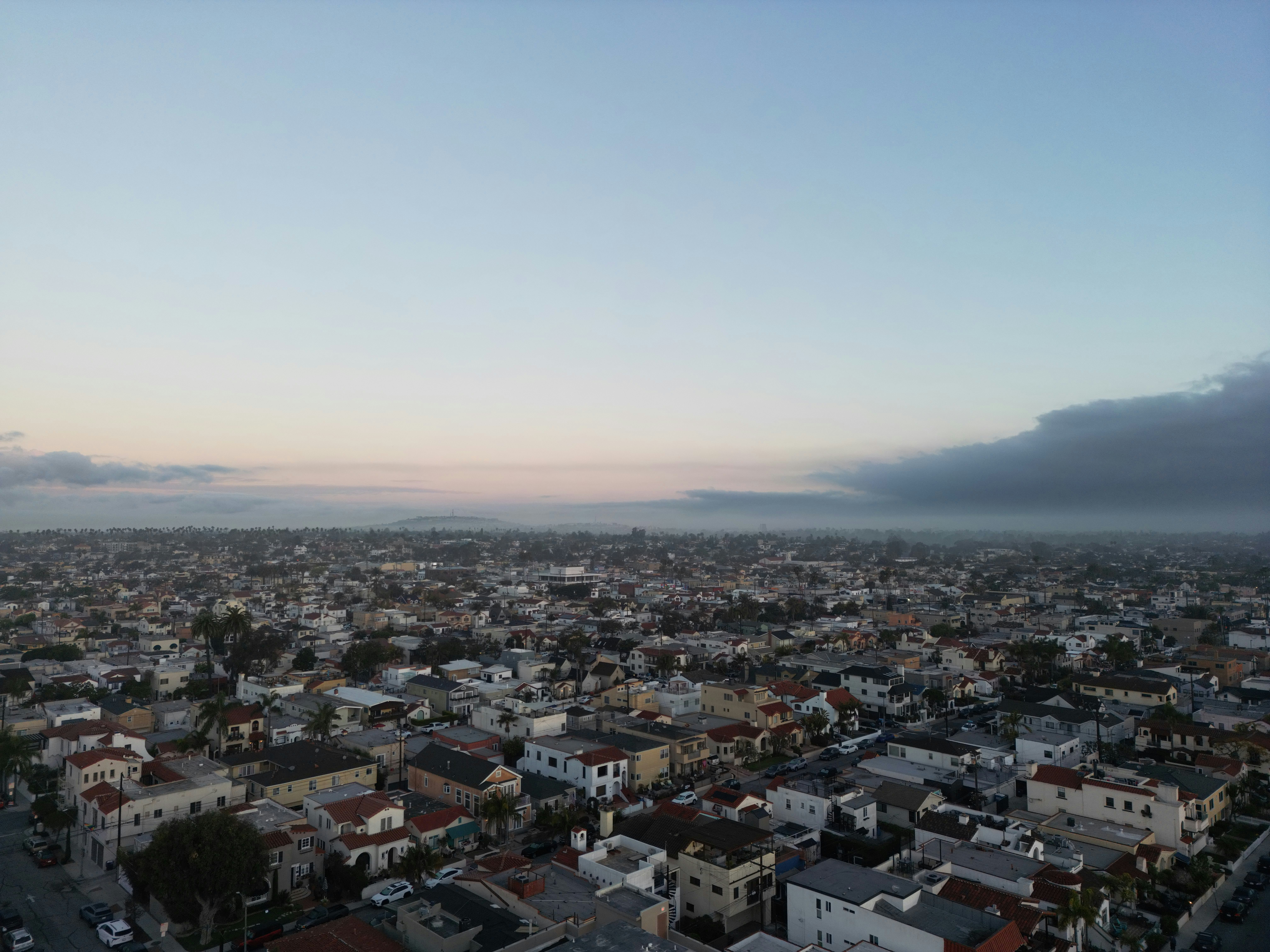 Aerial view of a suburban landscape at dusk with houses extending towards the horizon under a pastel sky.