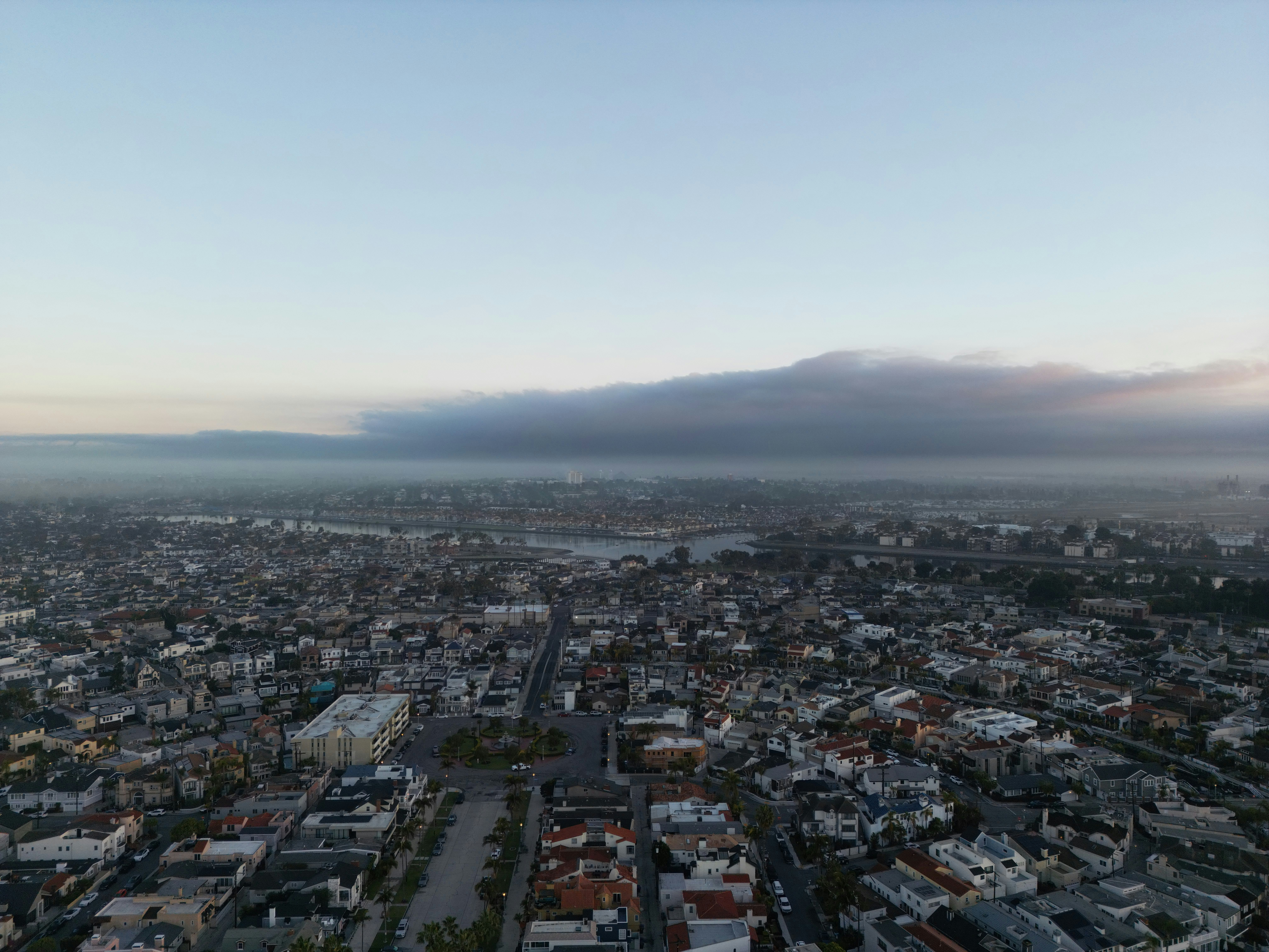 Sprawling cityscape under a twilight sky with distant mist and a network of rooftops and roads.