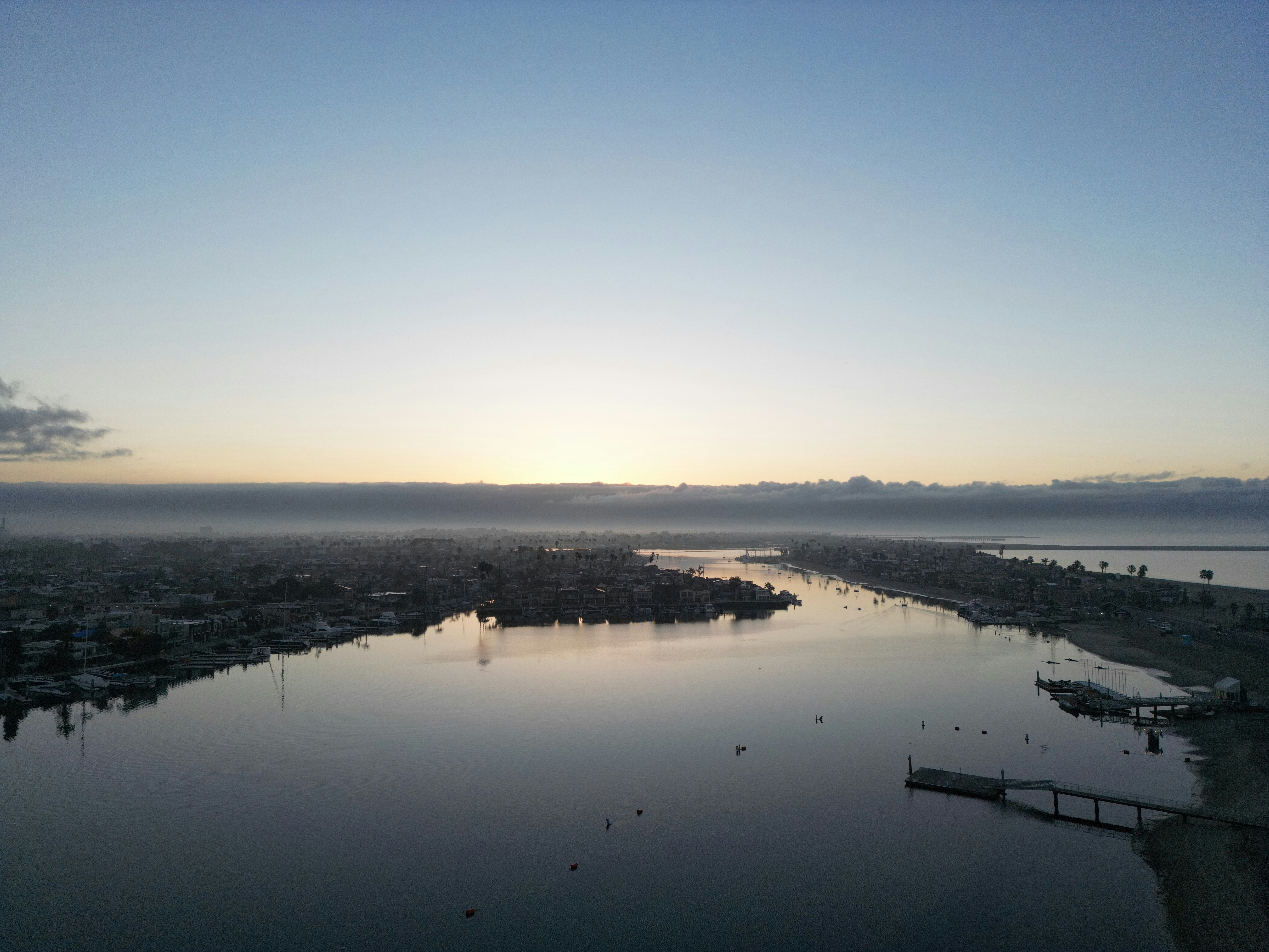 Aerial view of a serene coastal inlet at dawn with soft sunlight illuminating the shoreline and calm waters.