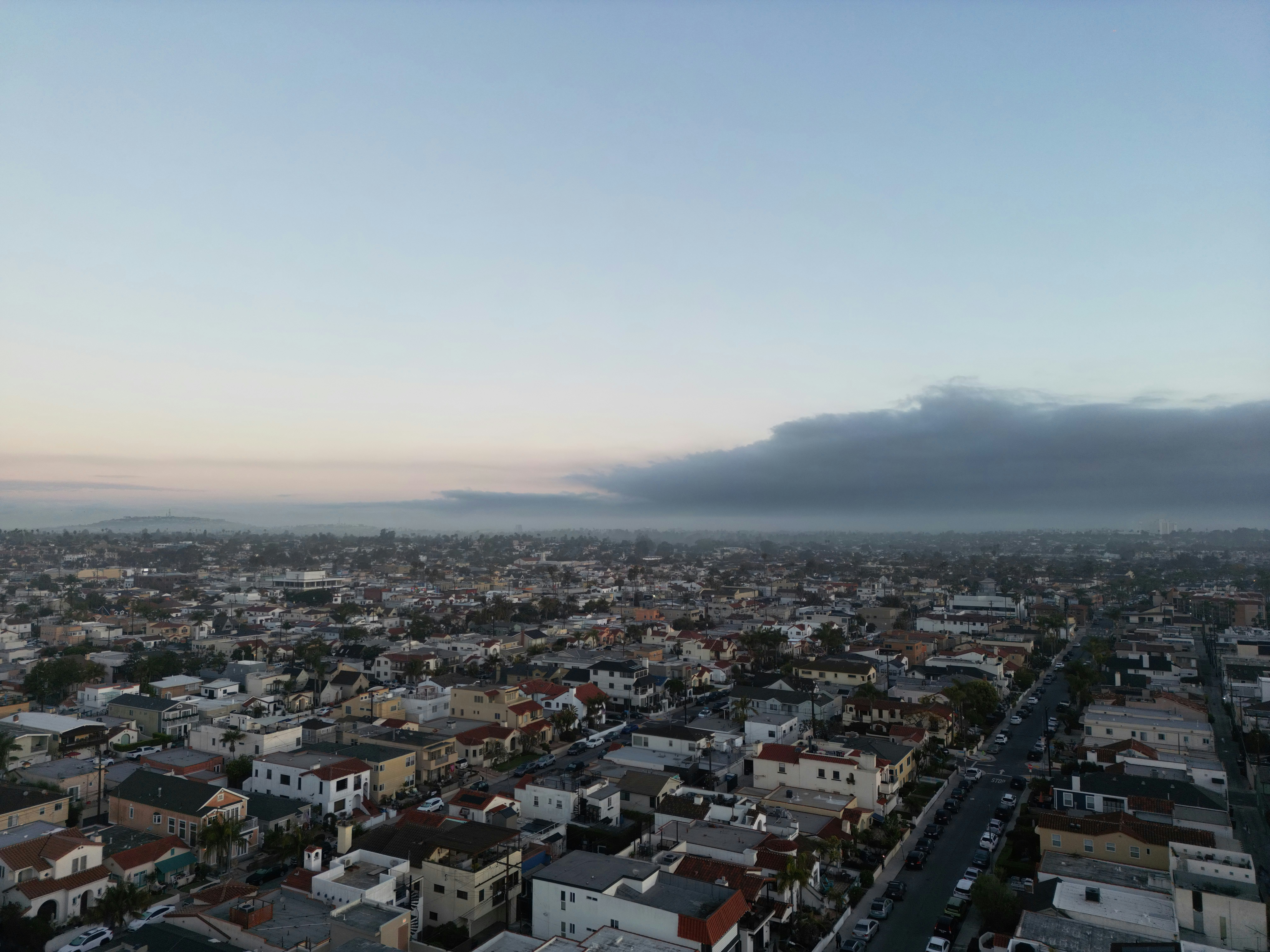 Urban landscape under a soft morning sky, with geometric rooftops and a gradient from orange to blue.