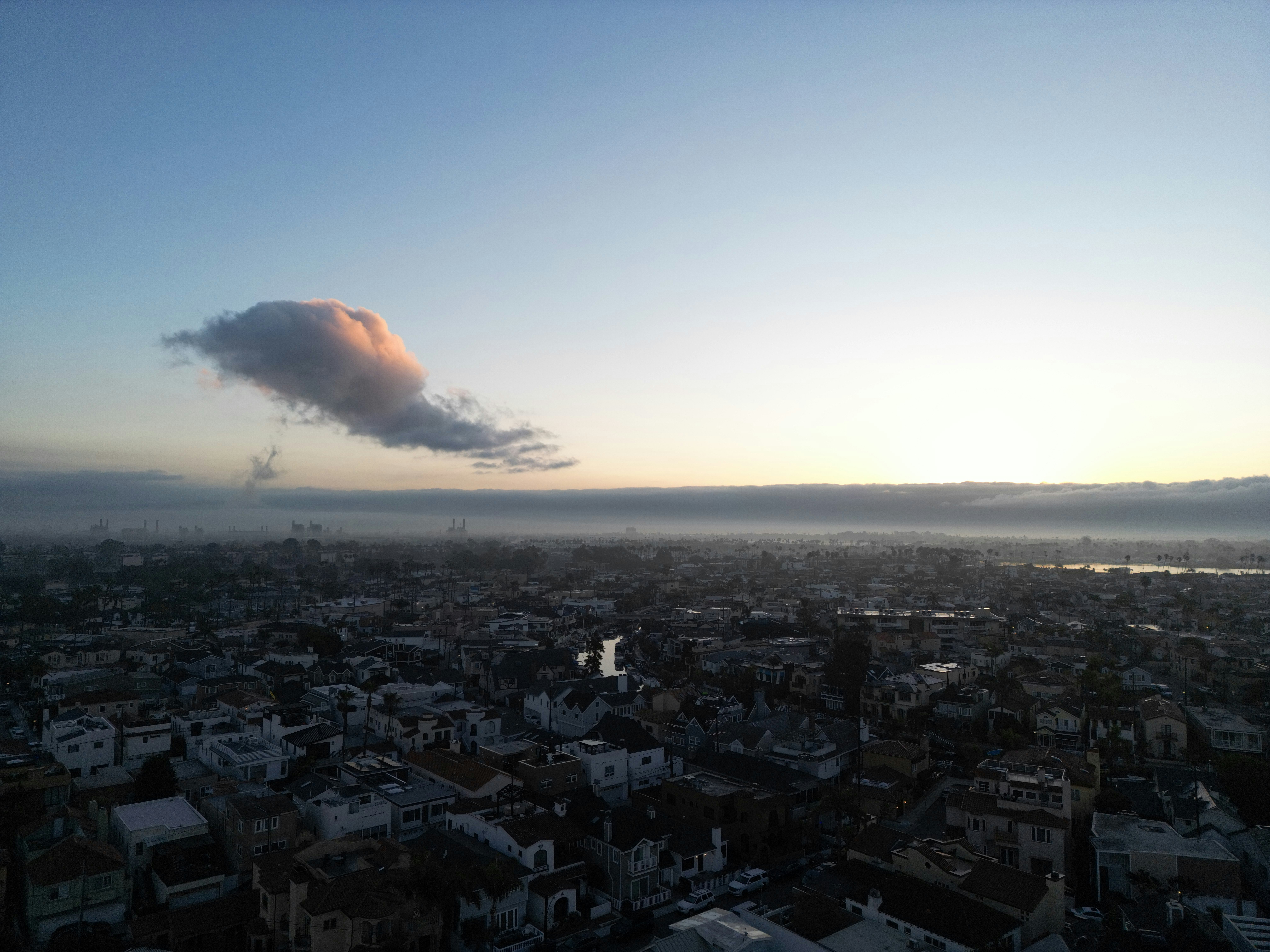 A solitary cloud floats above a waking city at sunrise, enveloped in pastel blues and oranges.