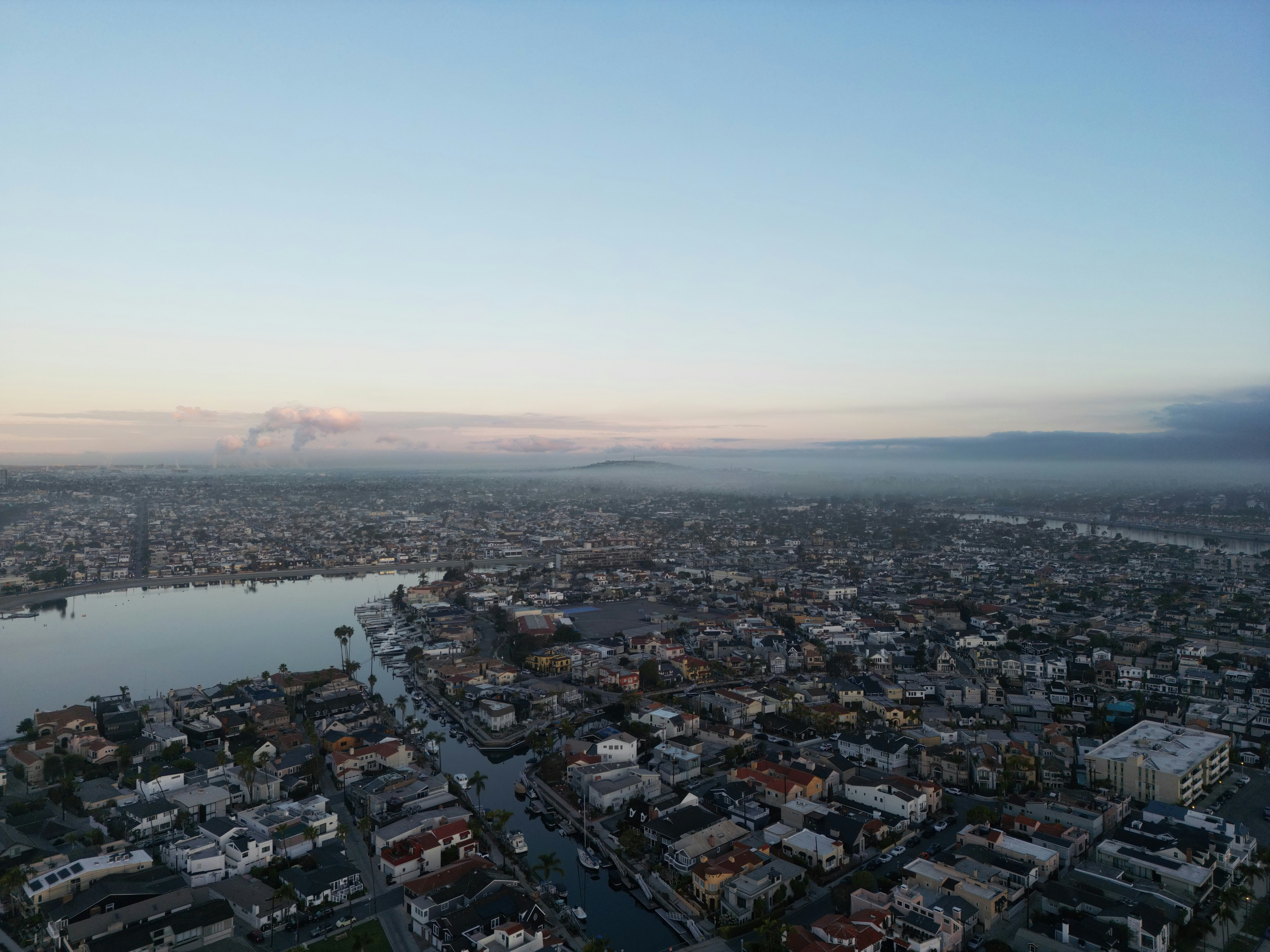 Aerial view of a city at dusk with a river interweaving through a dense urban landscape under a pastel sky.