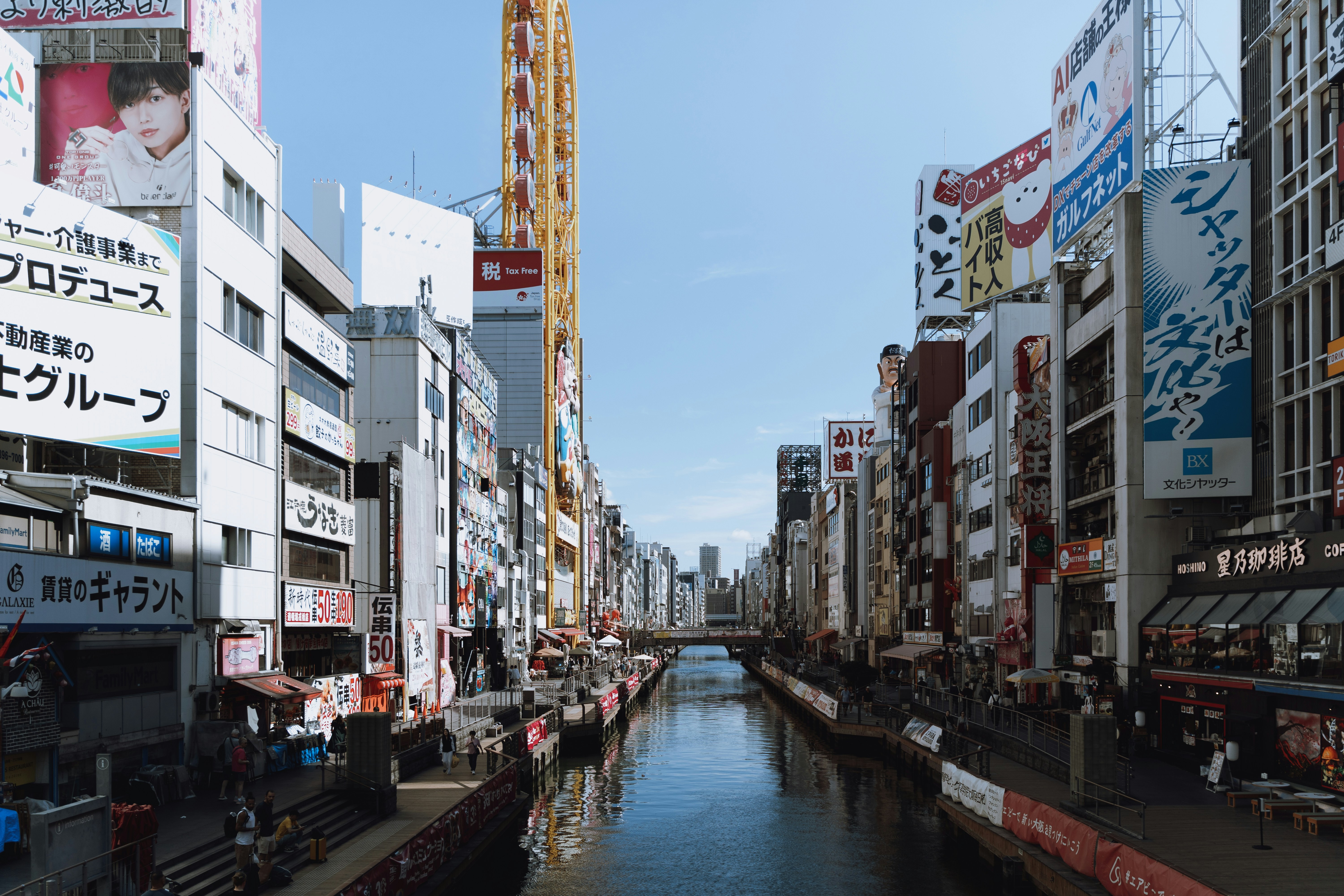 Urban canal flanked by colorful buildings and billboards under a clear sky.