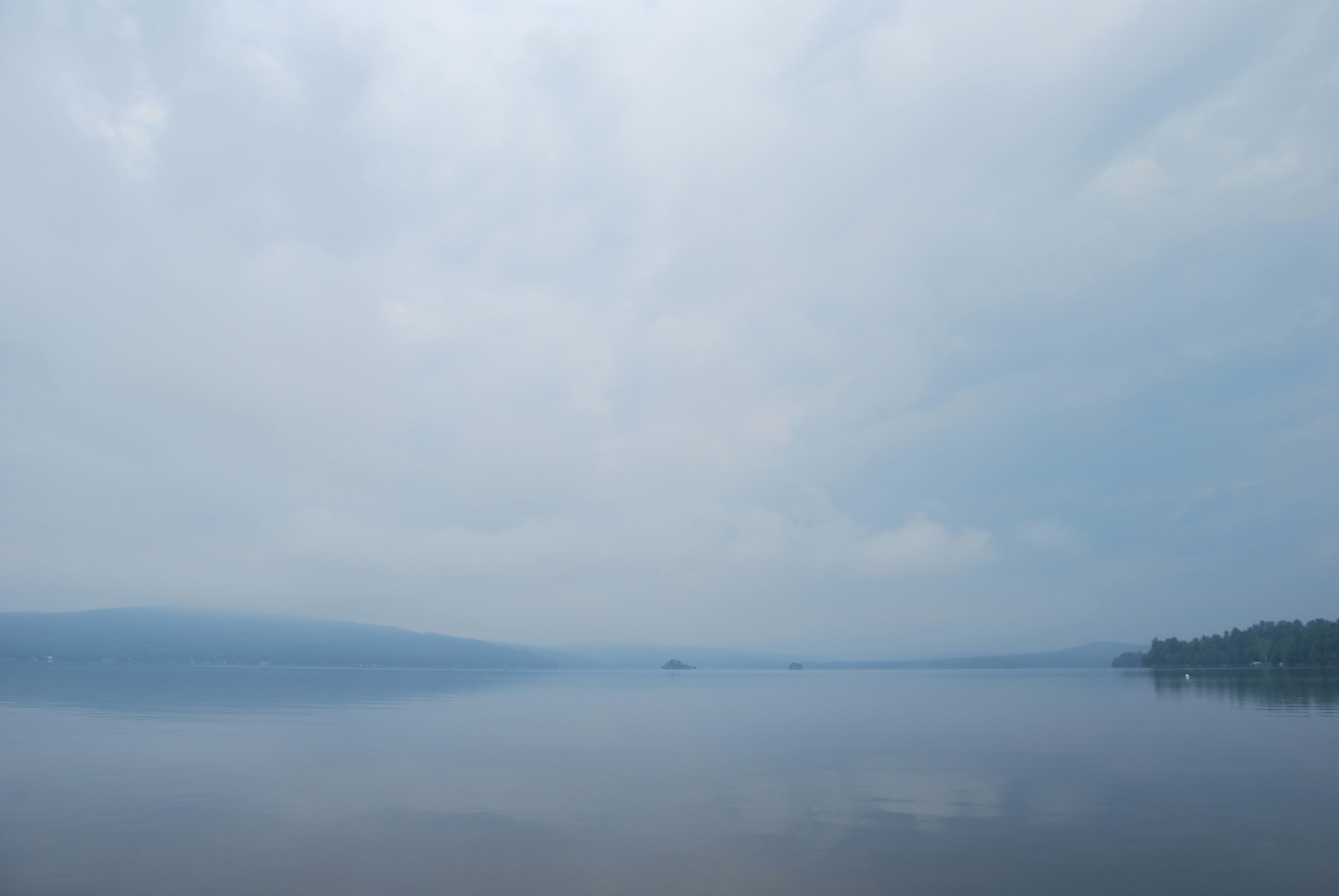 Misty lake reflecting muted blues and grays with distant hills barely visible.
