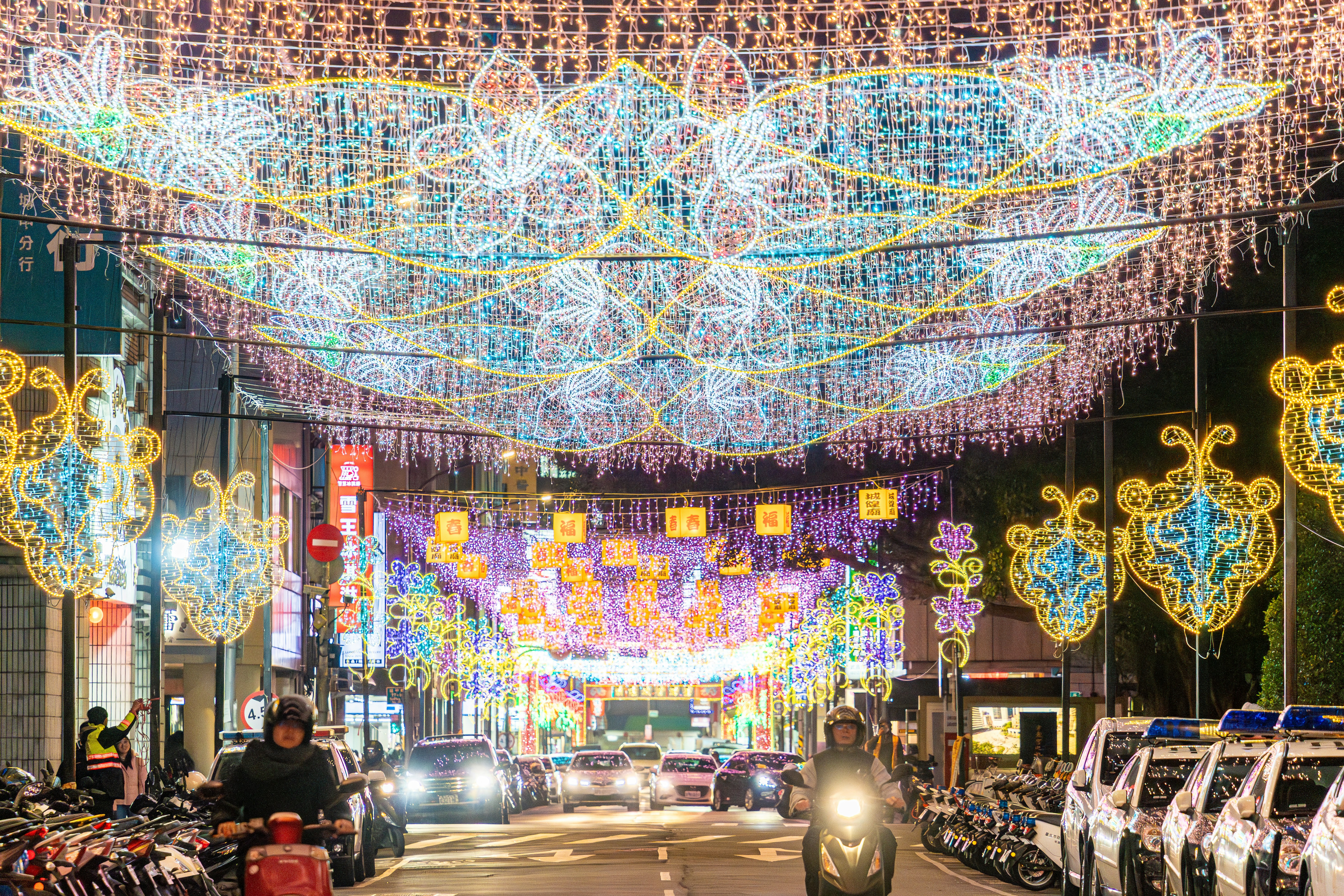 City street alive with colorful festive lights creating a vibrant canopy over bustling traffic.