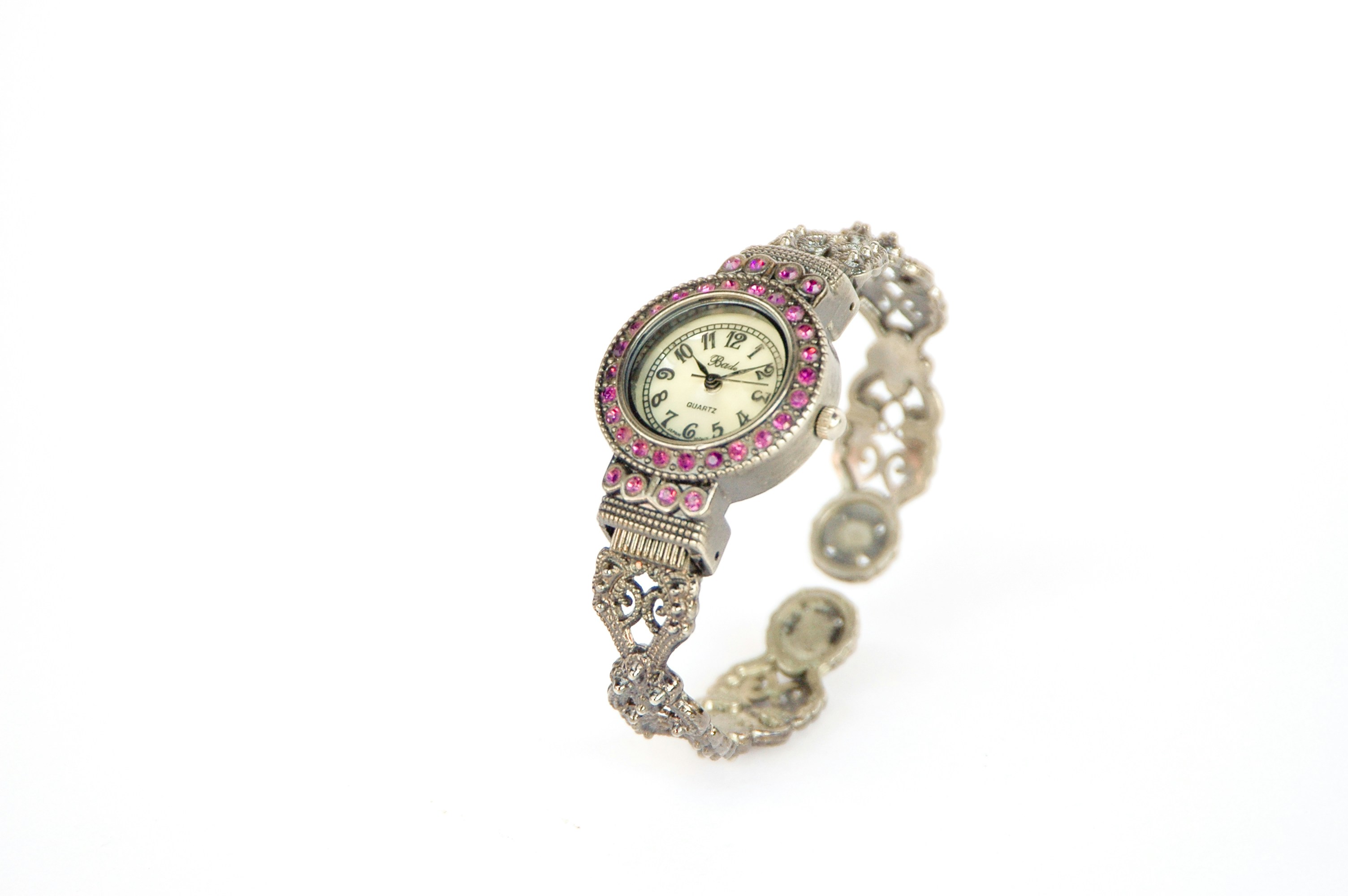 Vintage-style watch with pink gemstones and intricate metalwork on a white background.