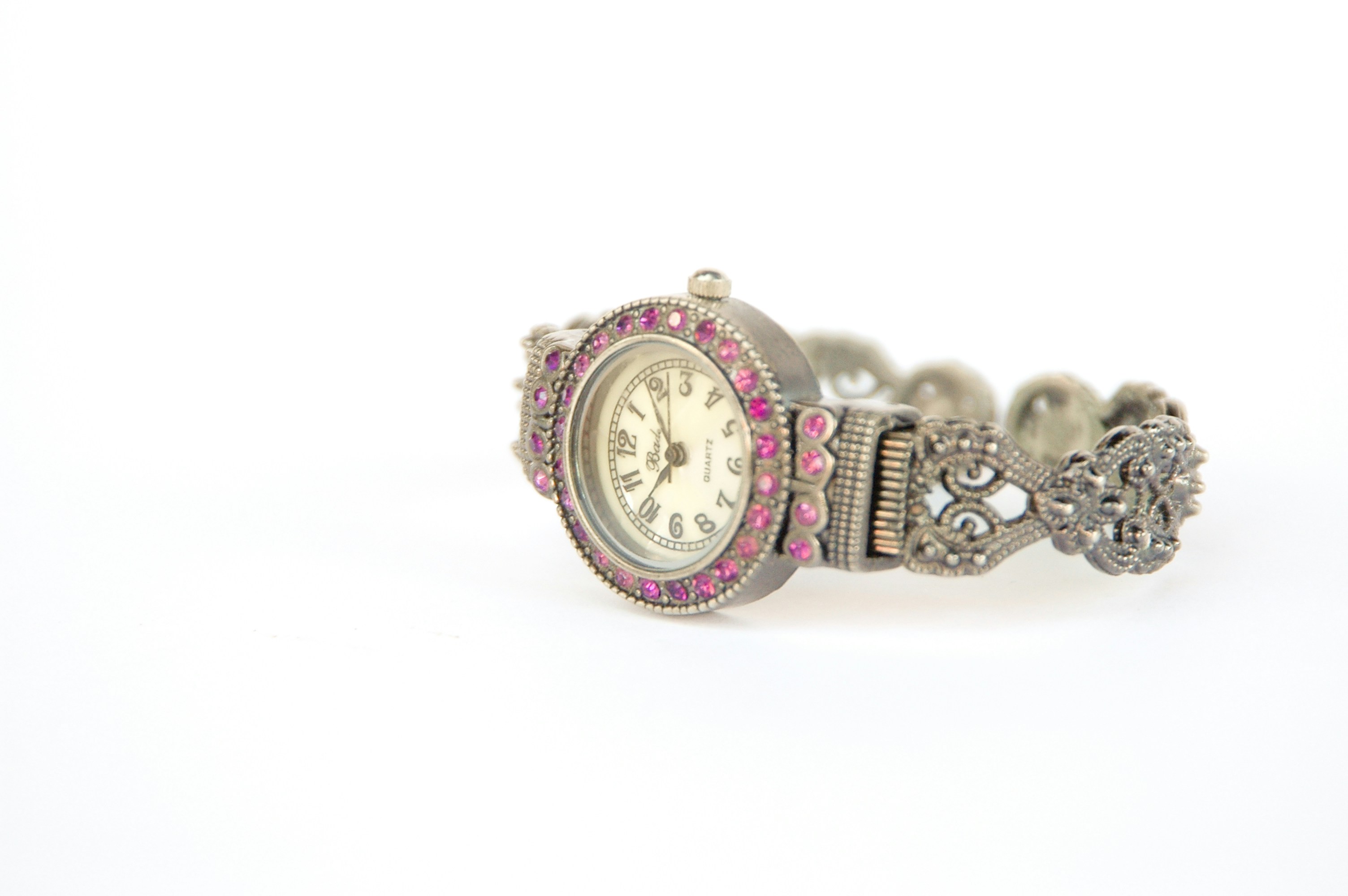 Intricately designed vintage watch with pink jewels on a soft white background.
