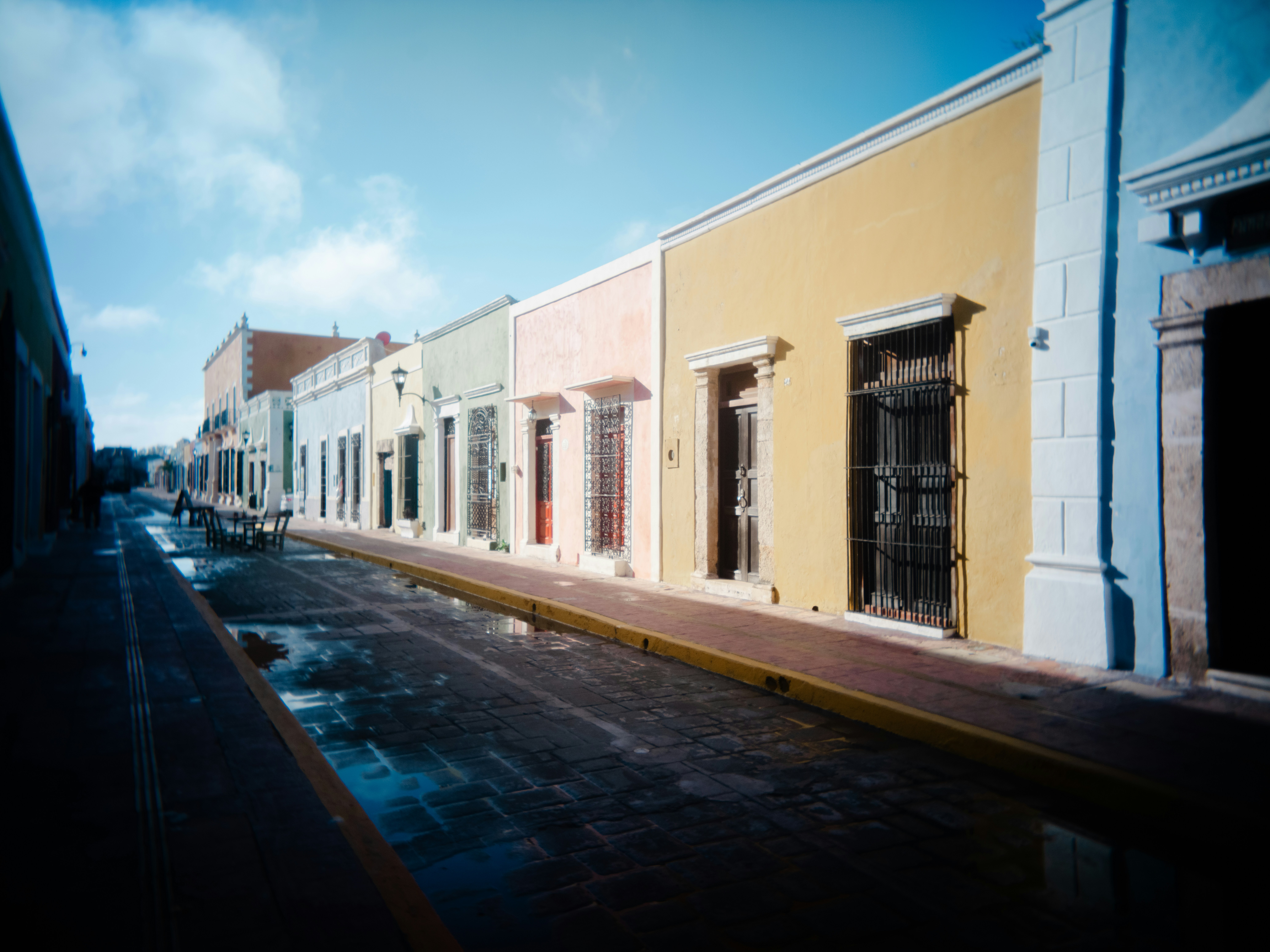Colorful row of colonial buildings lining a wet street under a bright blue sky.