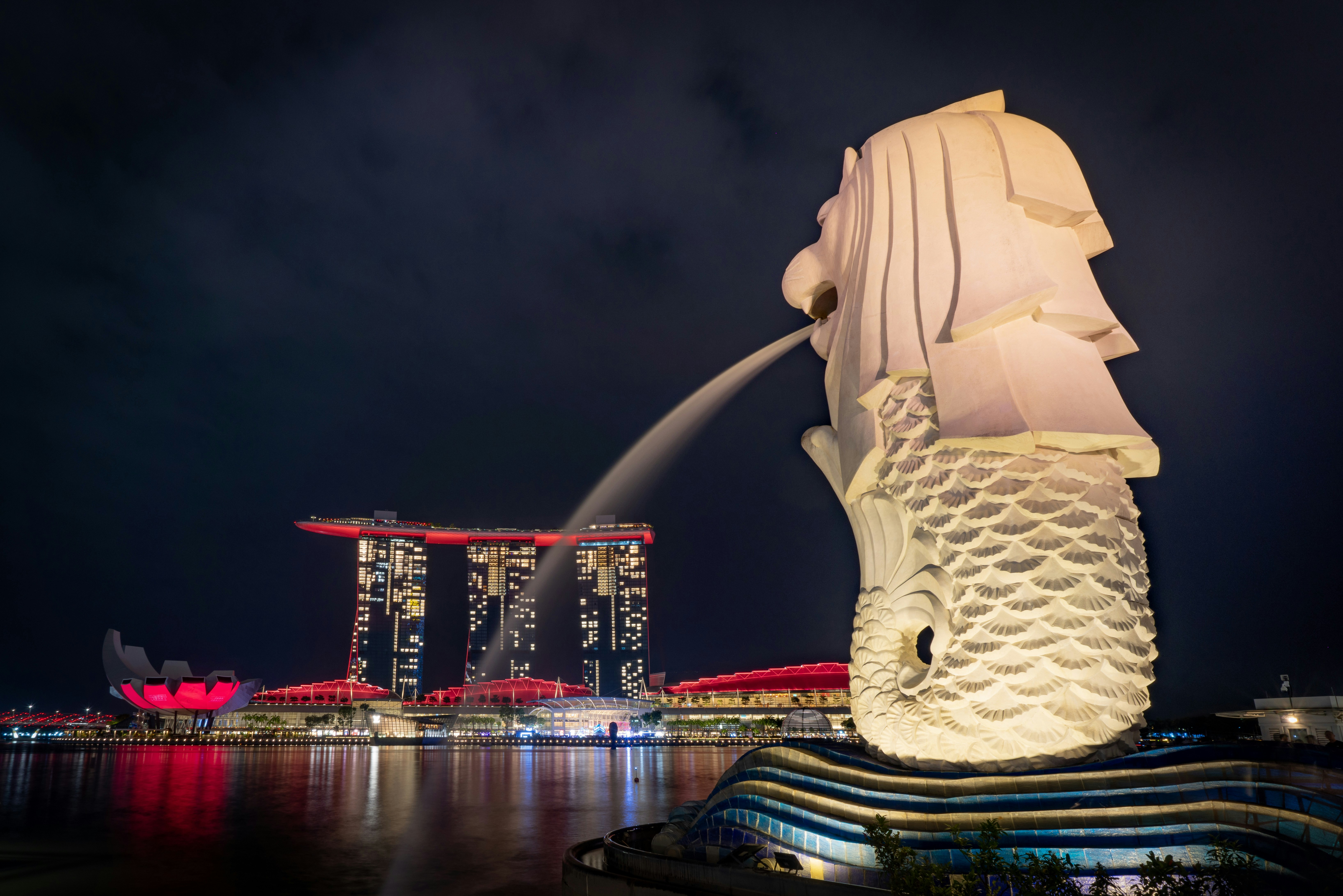 Merlion statue illuminated at night with Marina Bay Sands in the background under a dark sky.