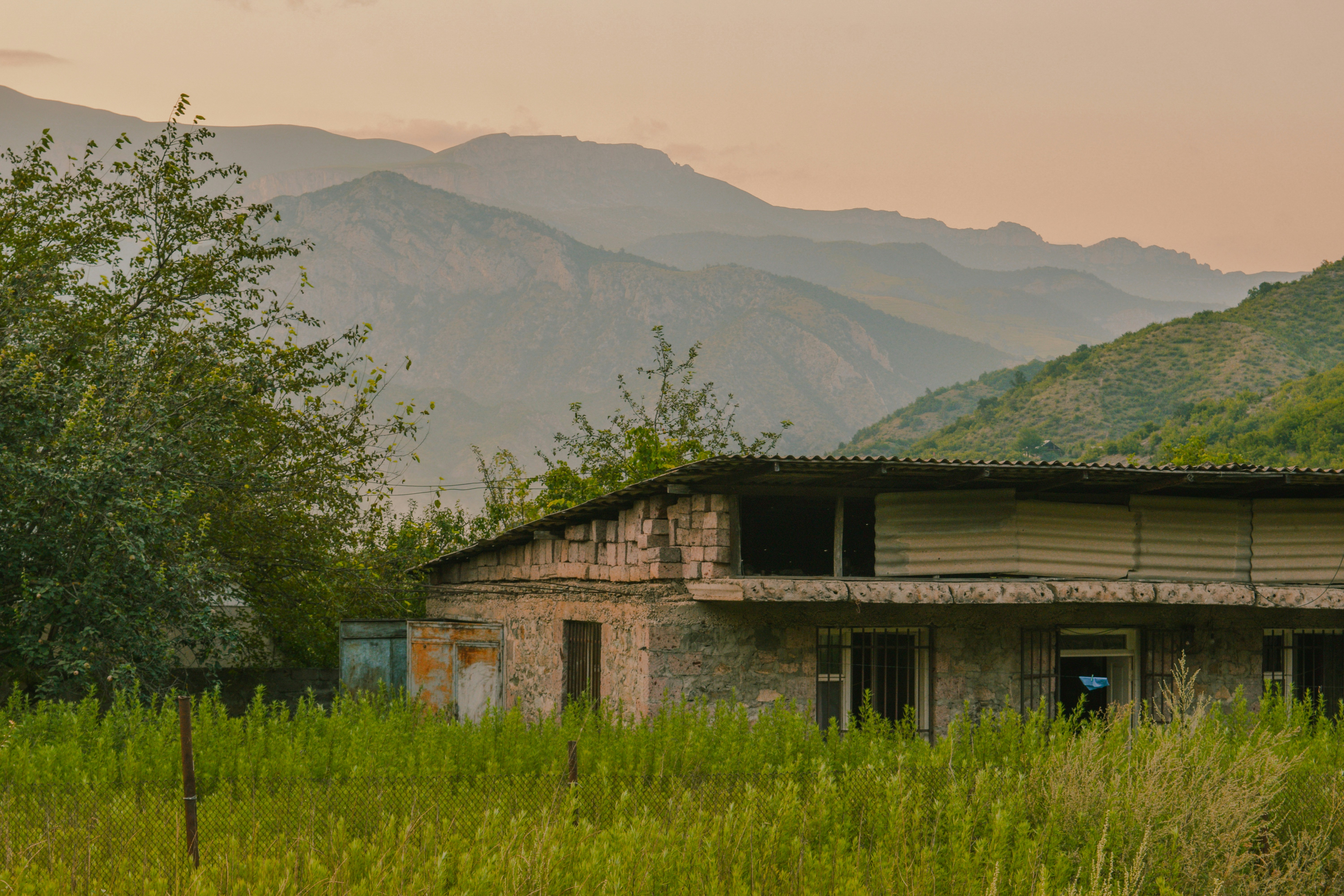 Stone building amid lush greenery with distant mountains under a dusky sky.