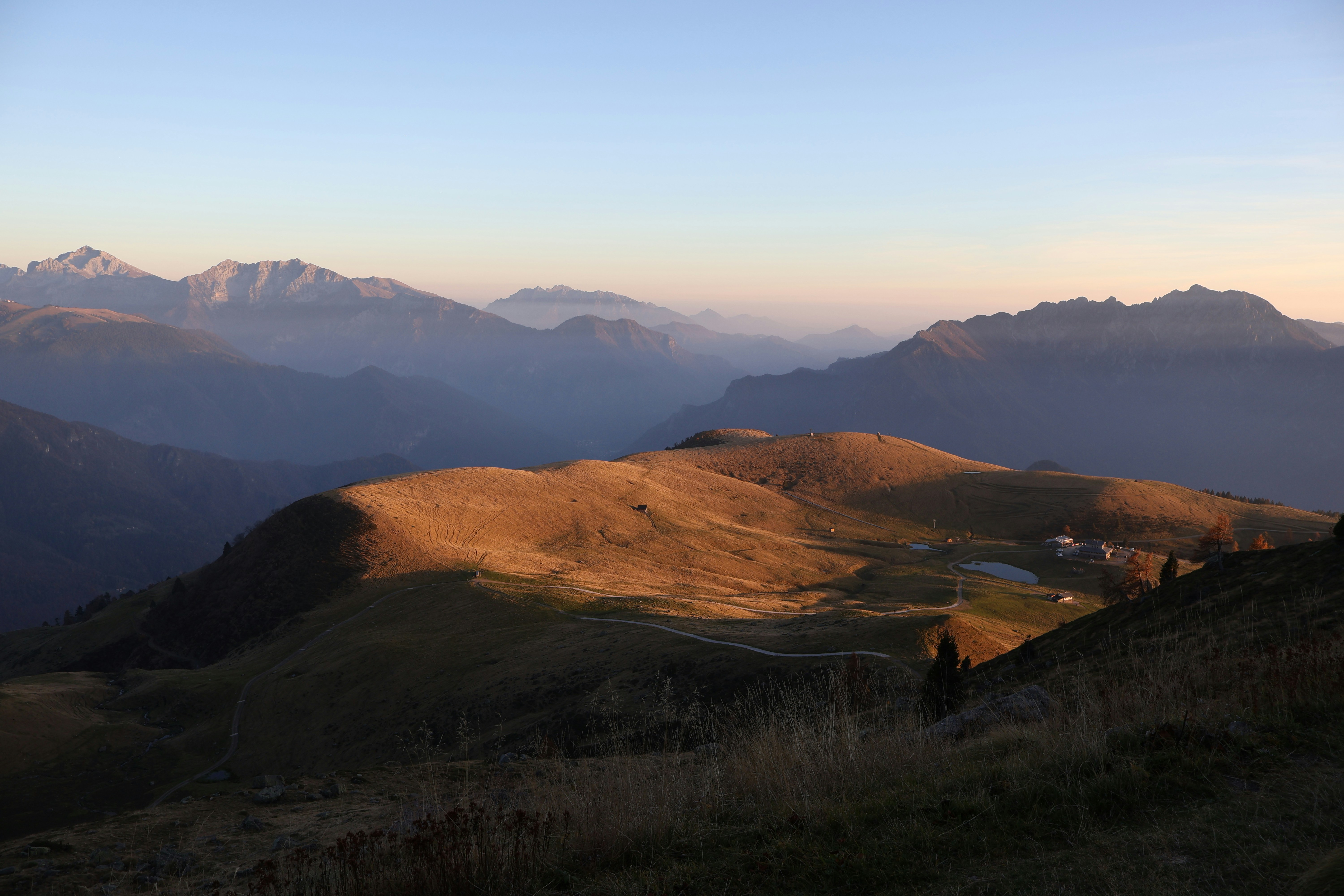 Warm sunset light bathes rolling hills, contrasting with shadowed slopes against distant mountain peaks.