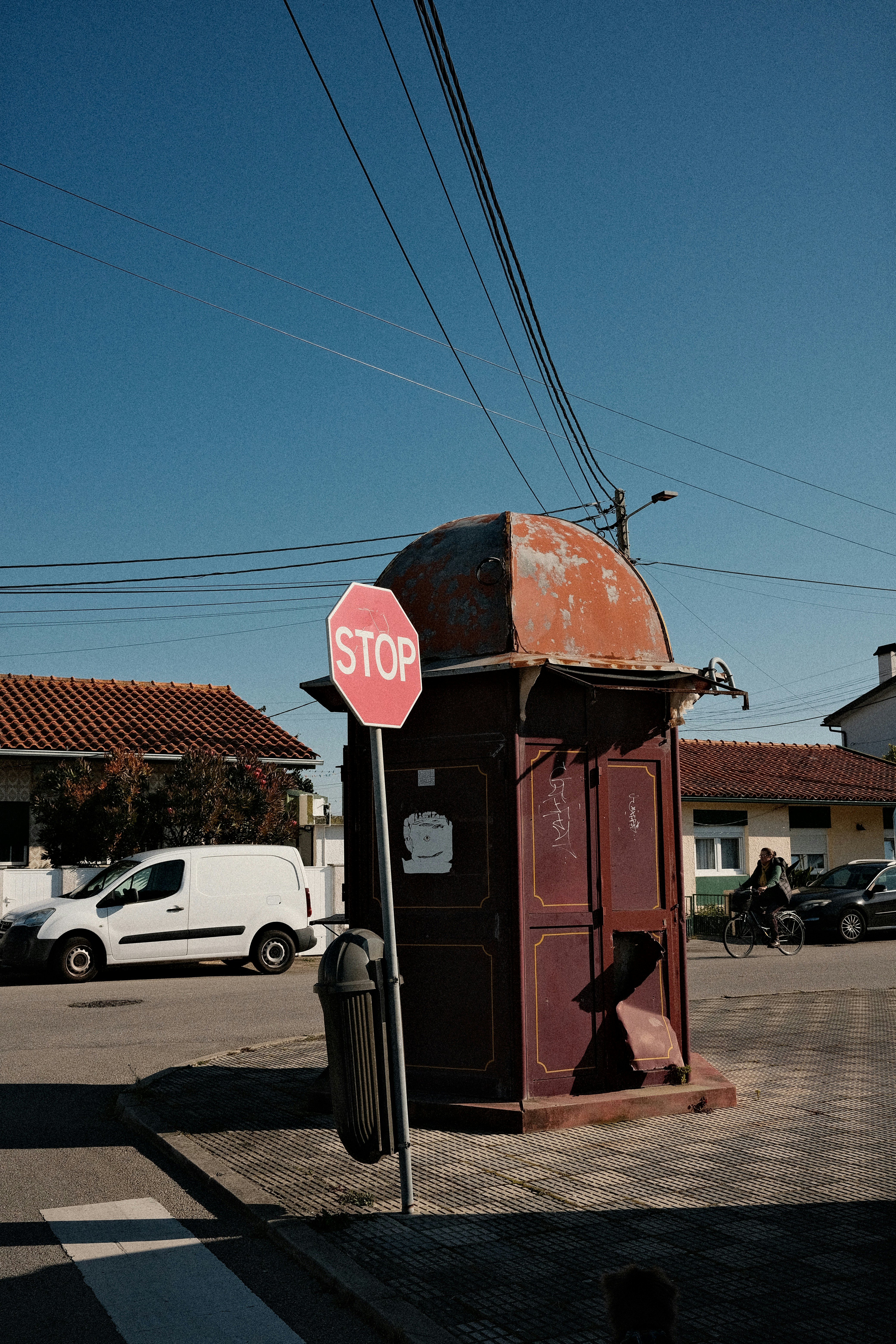 Crimson Stop Sign and a Weathered Kiosk on a Sunlit Street Corner
