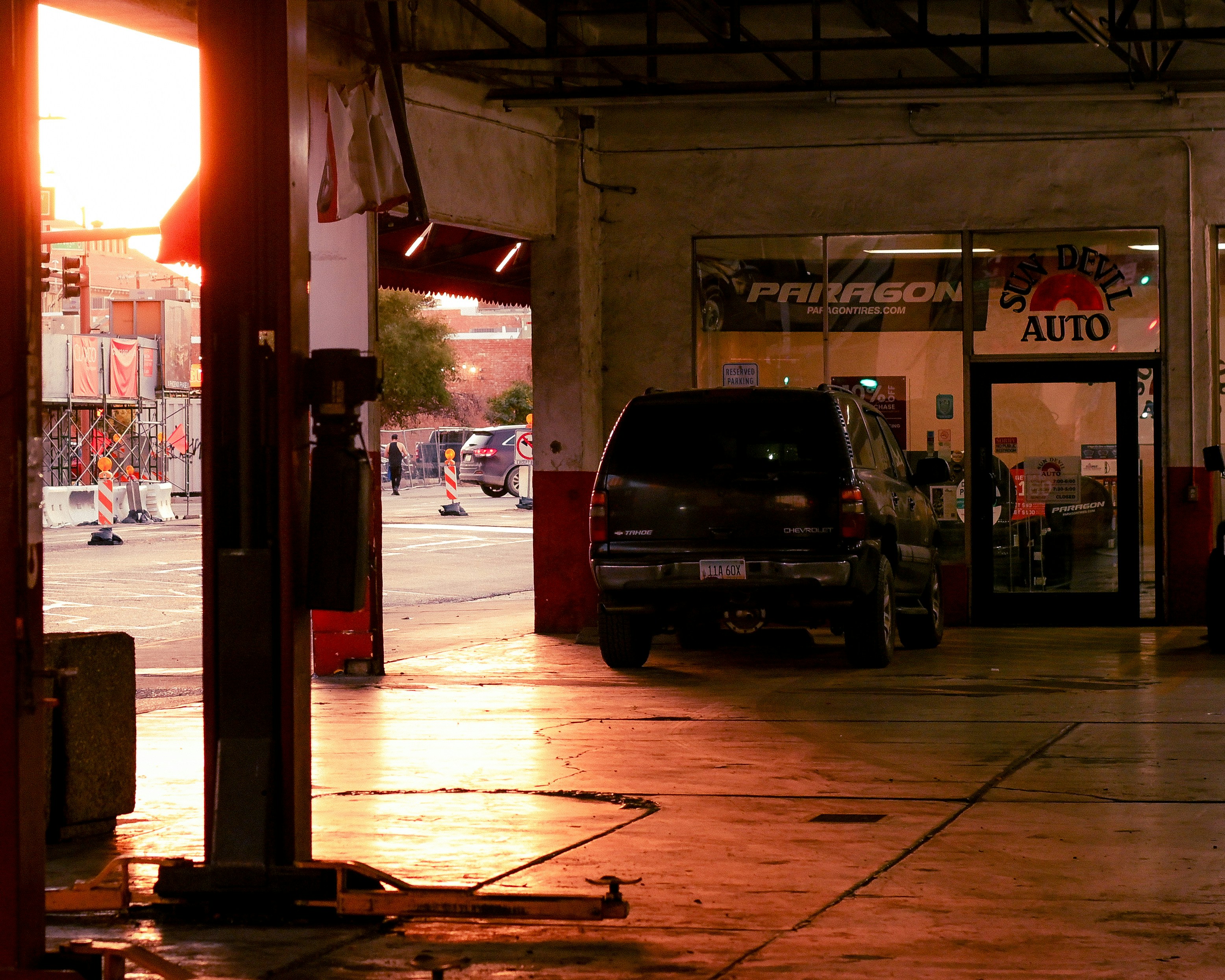 Warm sunset light bathes an auto shop interior, highlighting a parked SUV and contrasting with surrounding shadows.