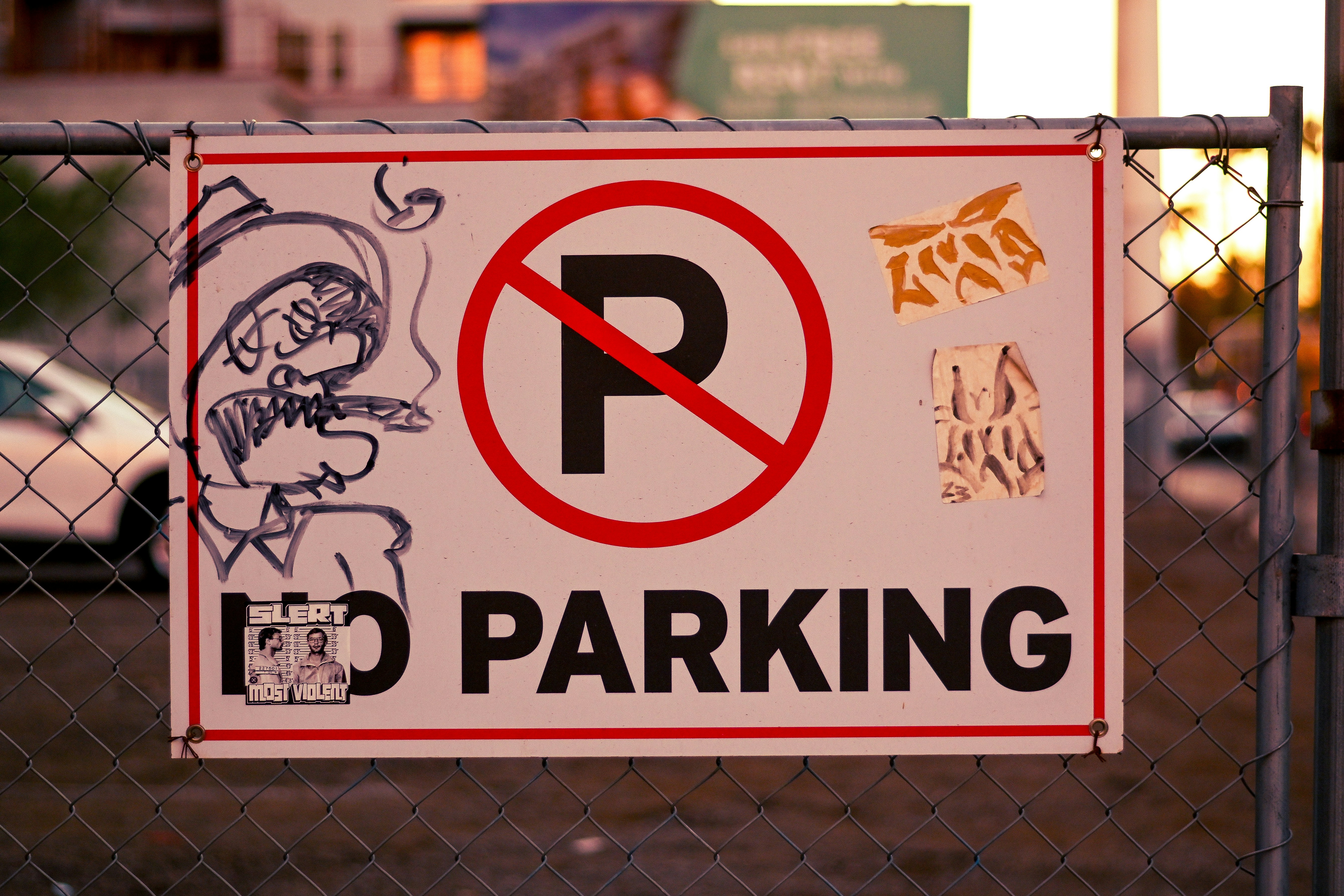Graffiti-Scarred No-Parking Sign Framed by Chain-Link