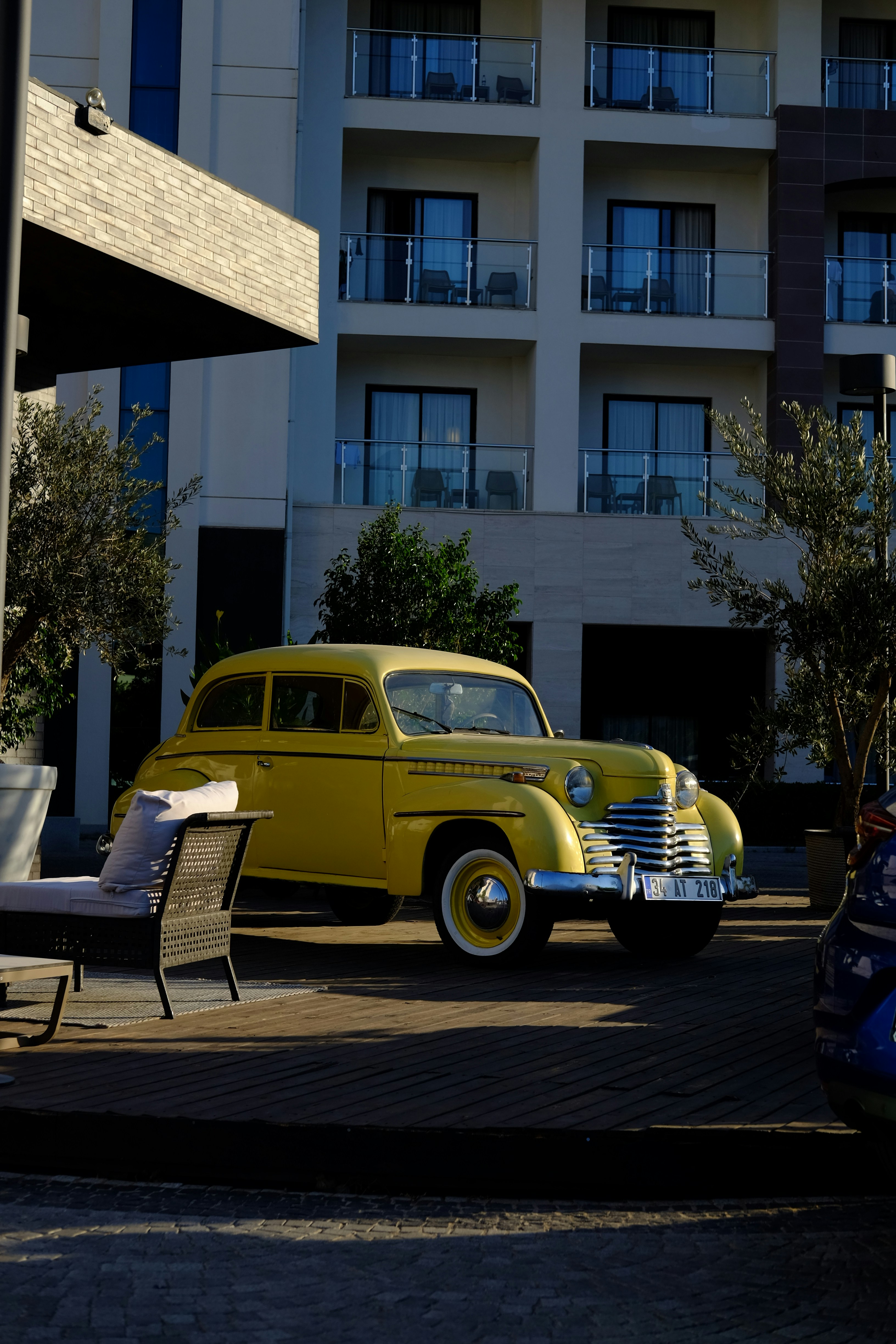 Sunlit Classic: A Yellow Chevrolet Resting by Modern Facades