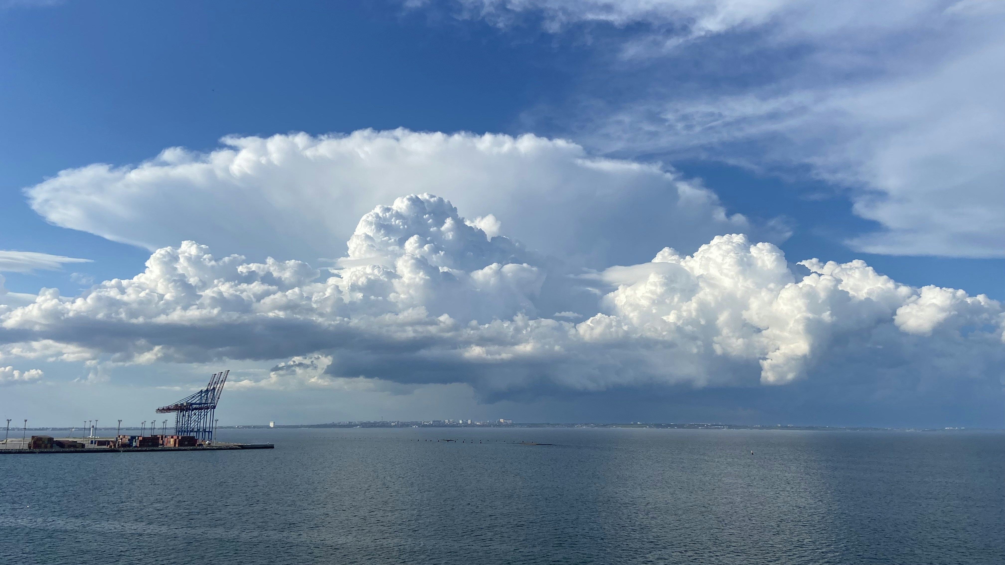 Cumulonimbus cloud formation looms over a calm harbor with a distant city skyline.