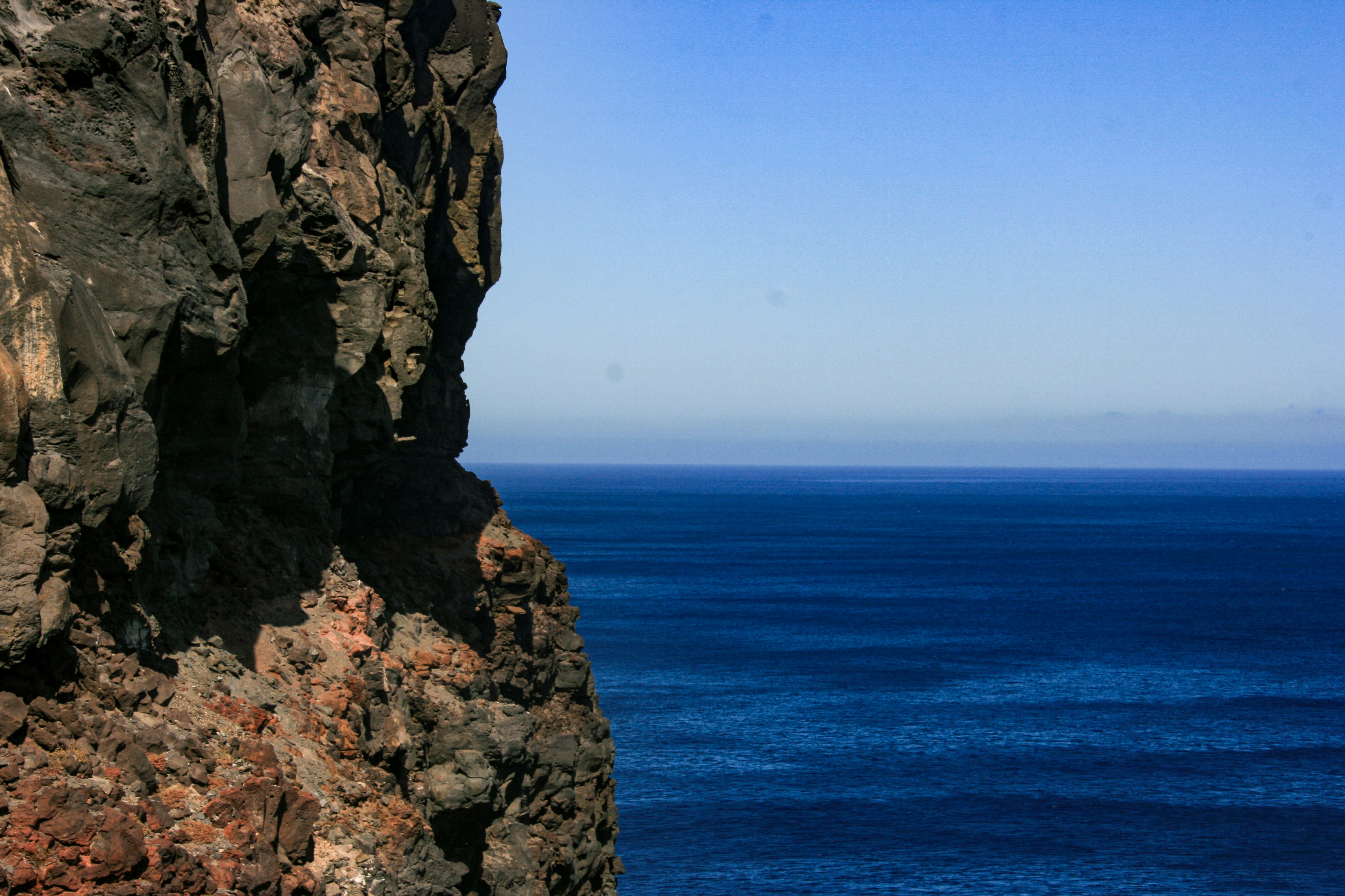 Rugged cliffside meeting the deep blue ocean under a clear sky.