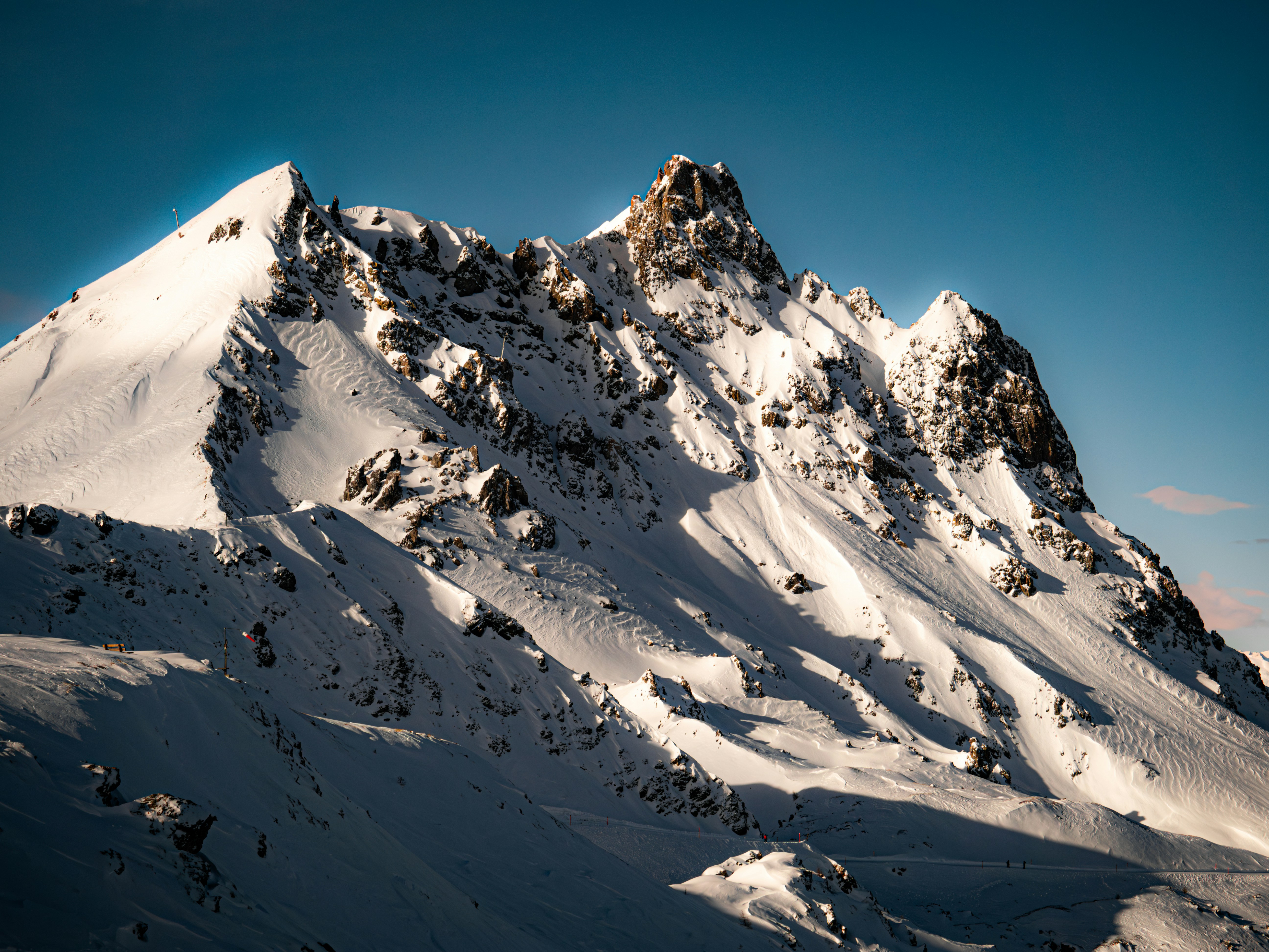 Snow-covered mountains illuminated by sunrise, with rugged peaks against a clear blue sky.