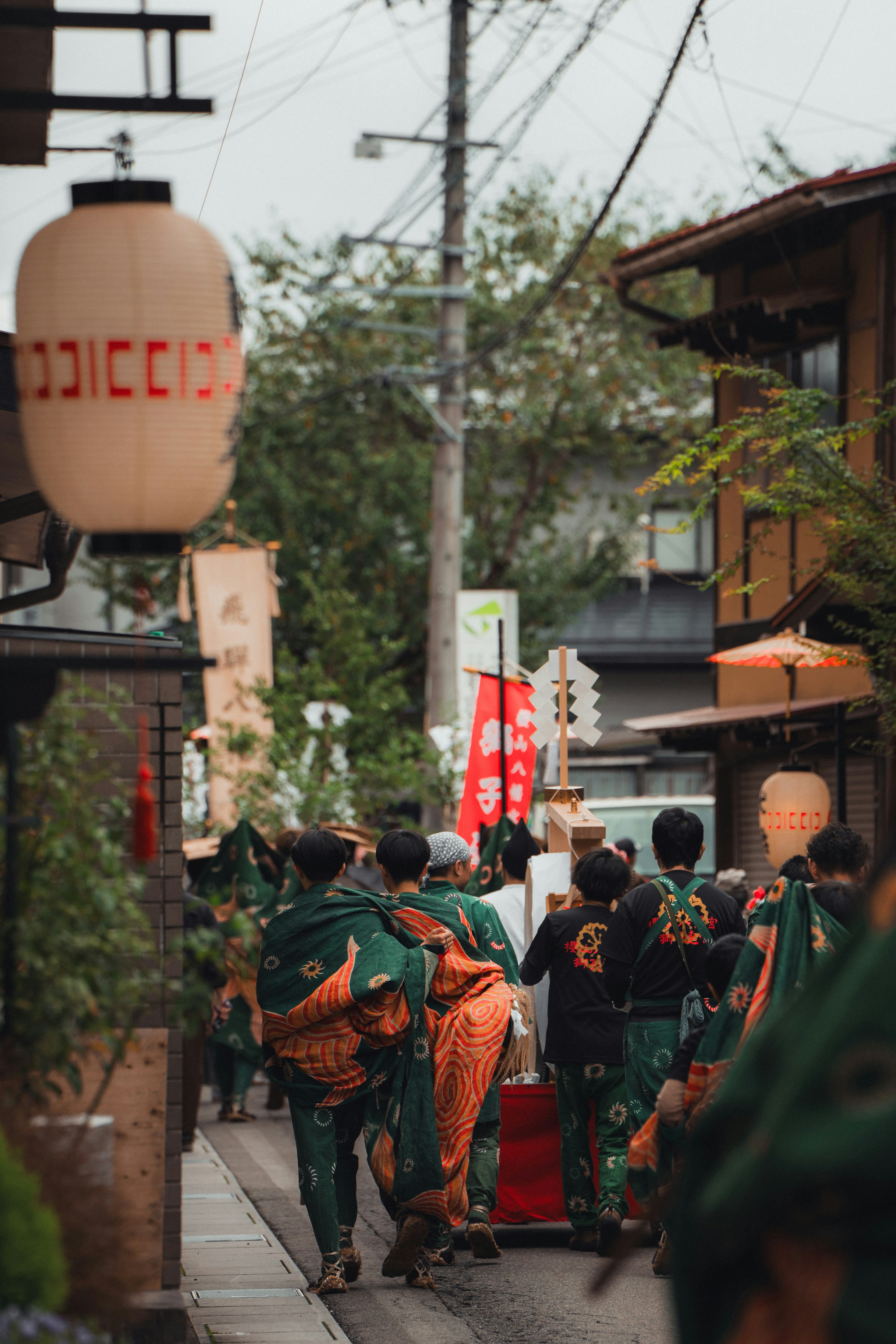 Emerald-clad procession under lanterns along a temple street
