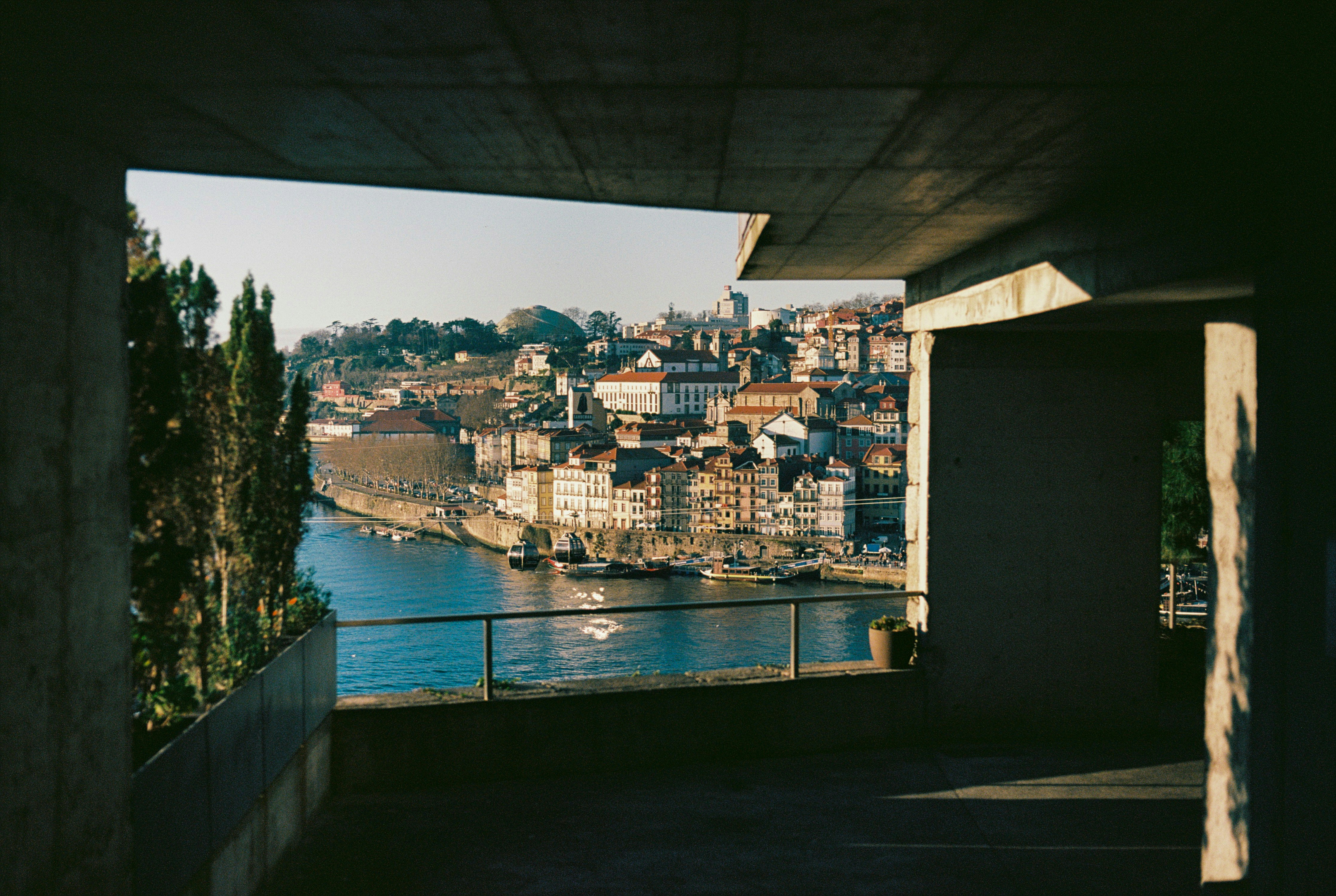 Cityscape along a river framed by modern architecture, with sunlight illuminating historic buildings and contrasting with the blue water.