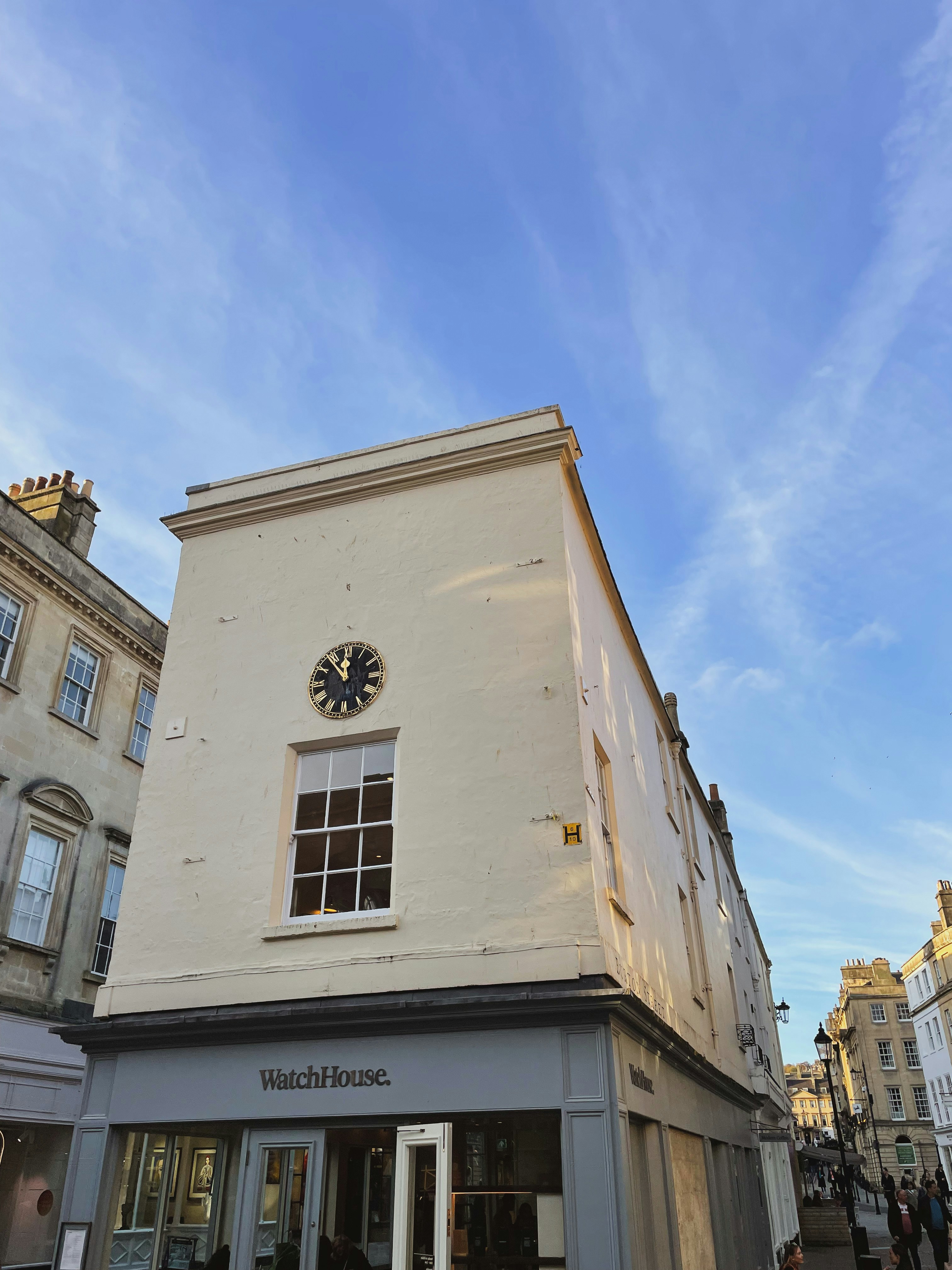 Historic corner building with a clock under clear blue skies and wispy clouds.
