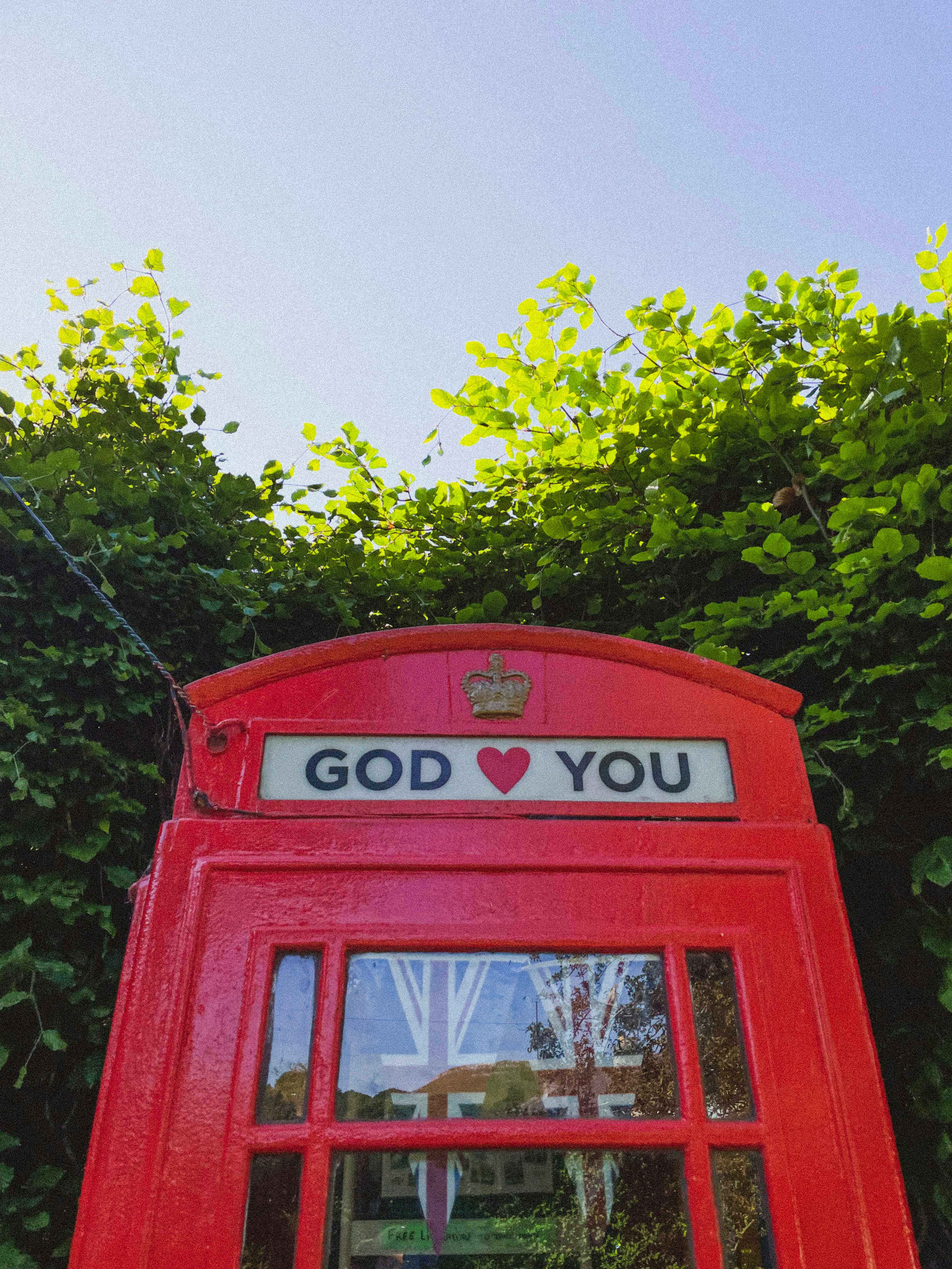 Crimson UK Post: A Bold Red Phone Booth Framed by Lush Greenery