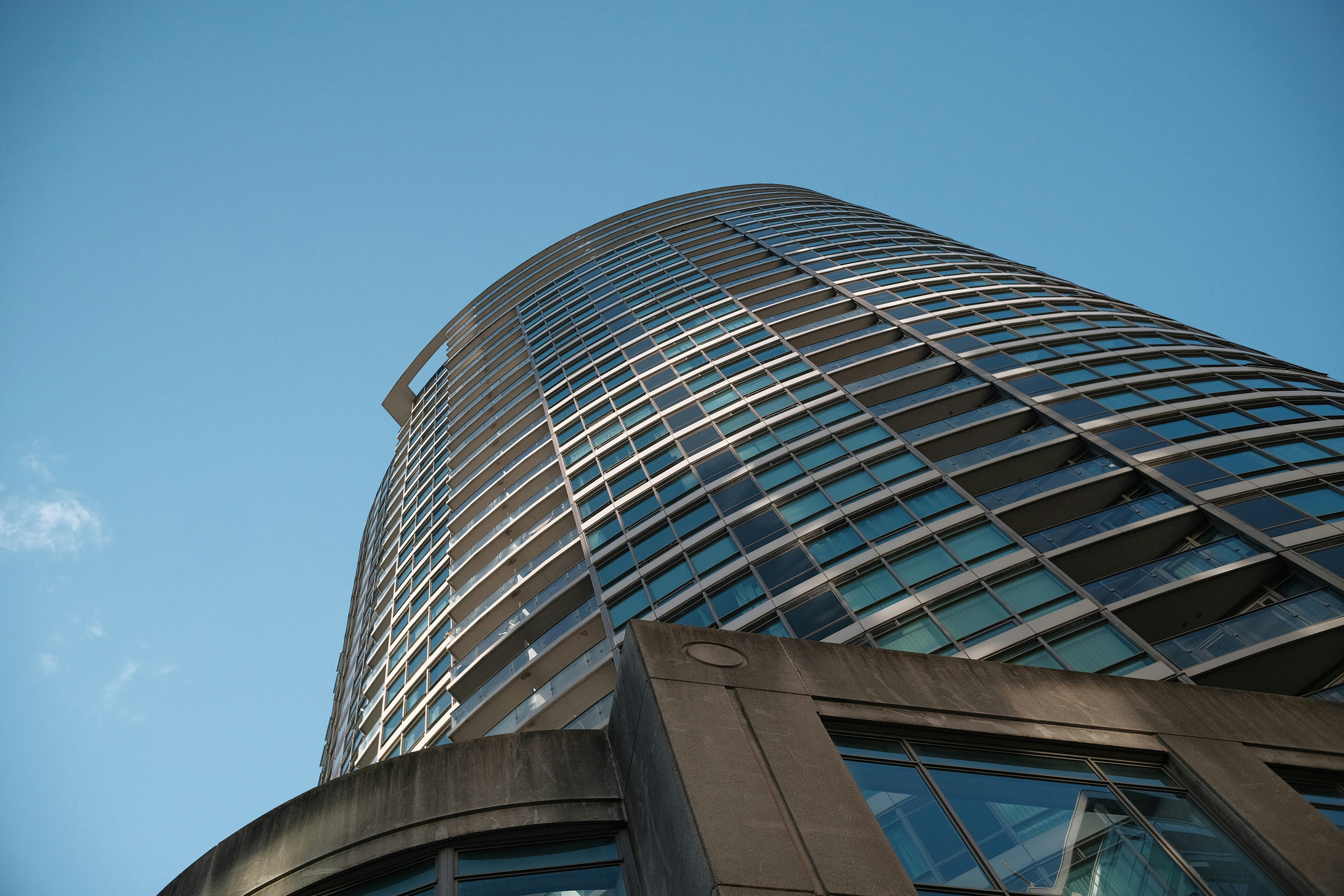 Modern skyscraper viewed from below against a clear blue sky, showcasing its sleek glass facade and dynamic architectural lines.