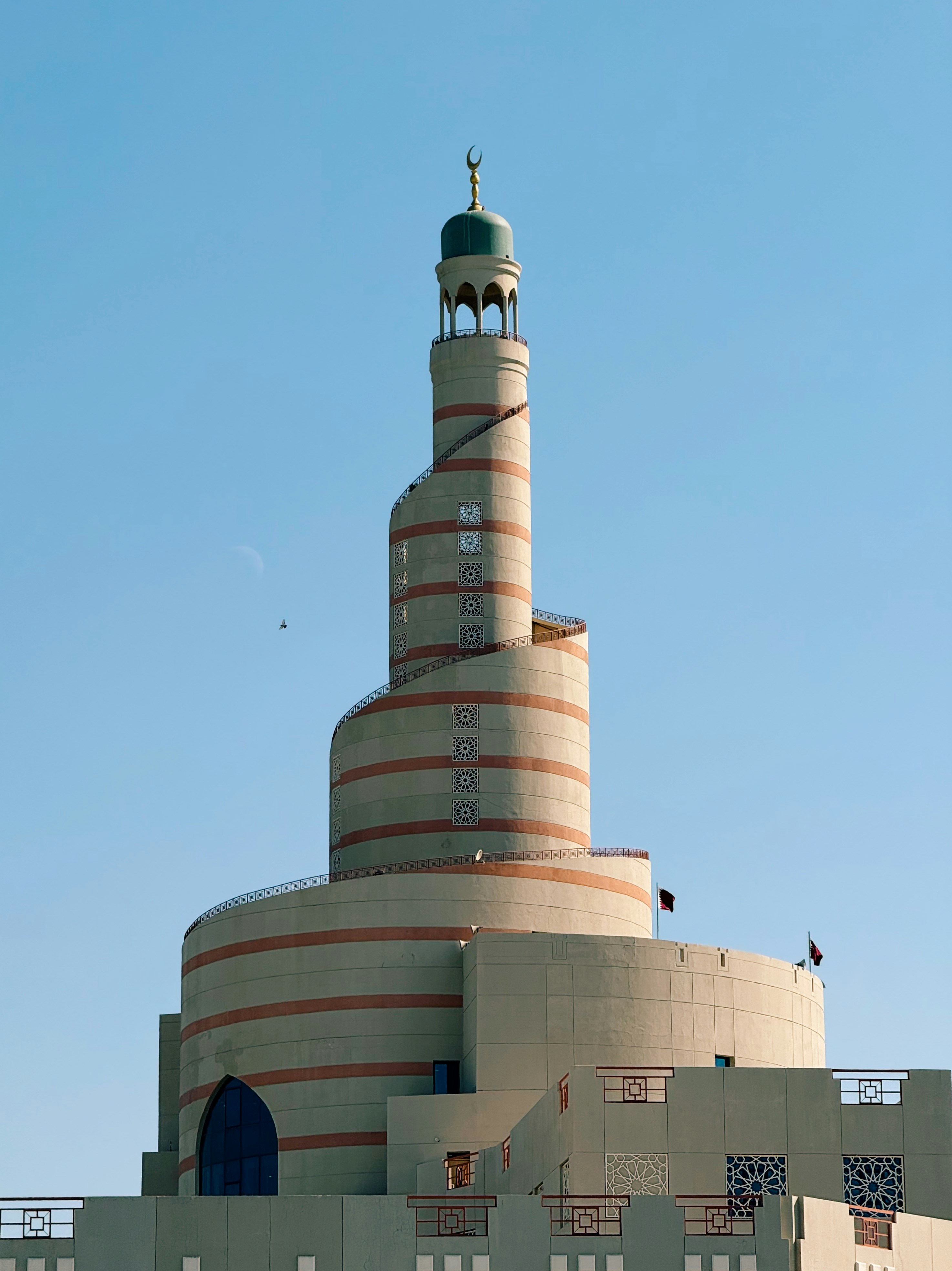 Spiraling, striped tower rises against a pale blue sky, an architectural photograph highlighting its concentric geometry and rounded base.