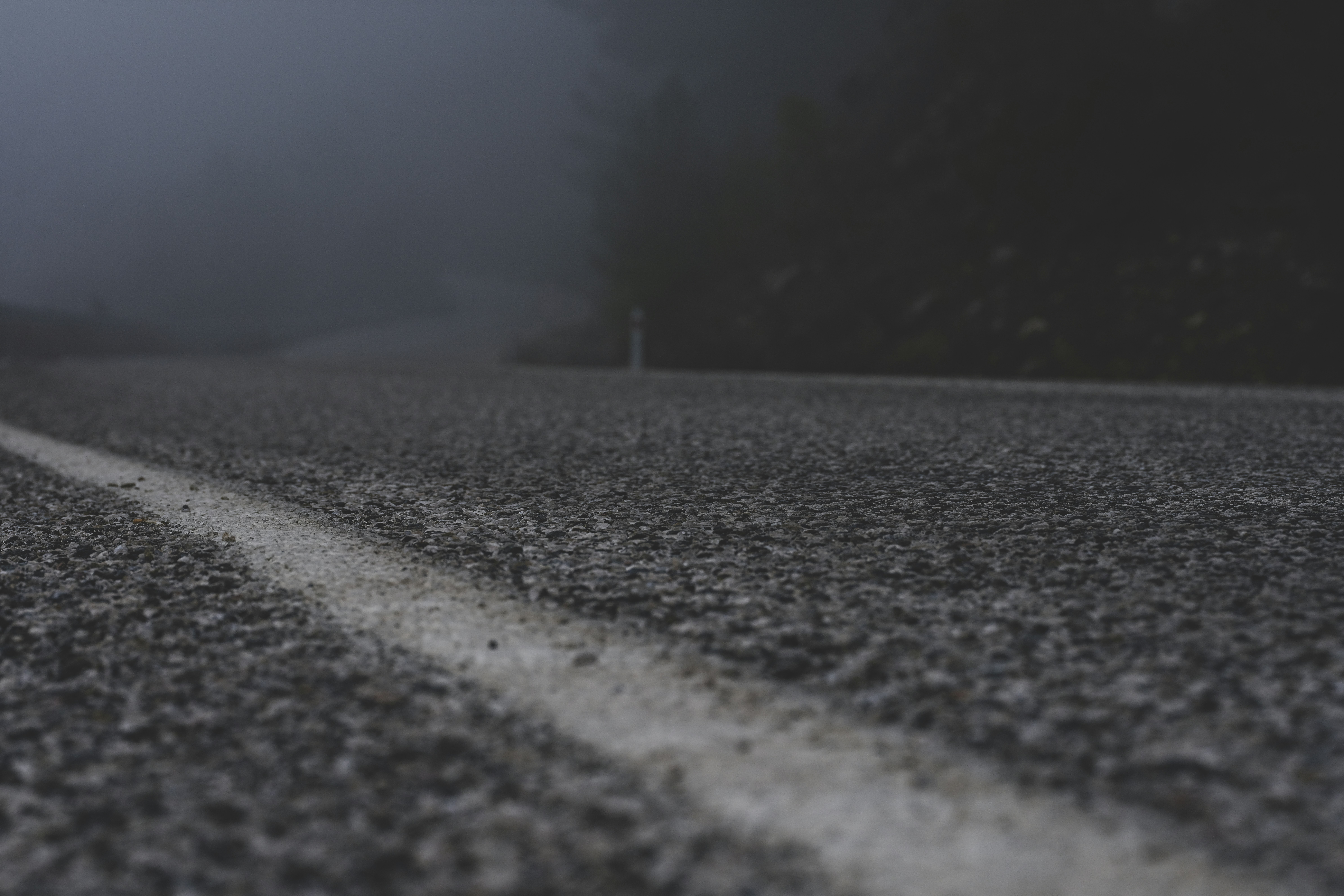 Desolate road vanishing into thick fog, highlighting solitude with textured asphalt in the foreground.