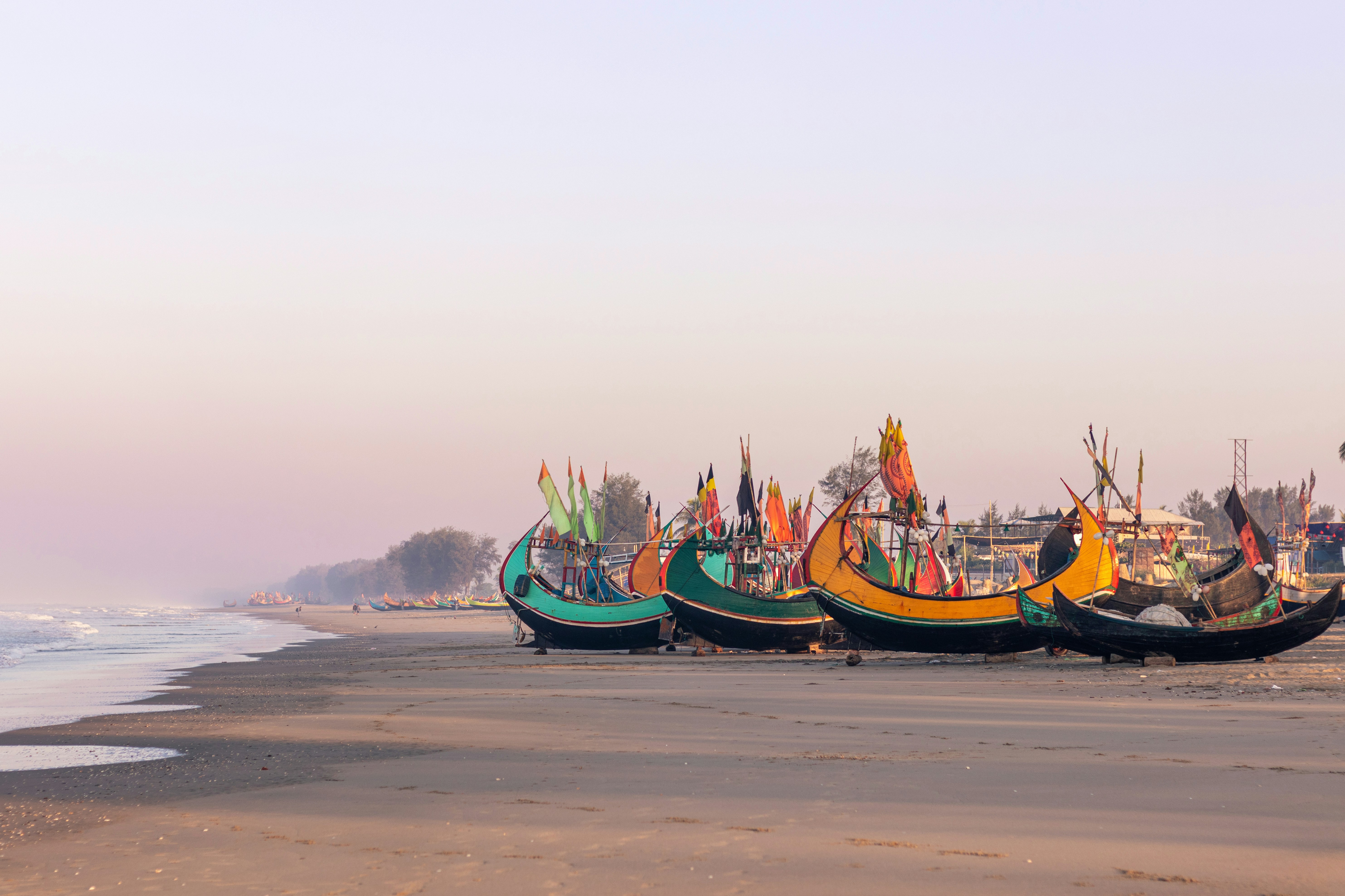 Vivid fishing boats with colorful sails lined along a serene beach under a soft dawn sky.