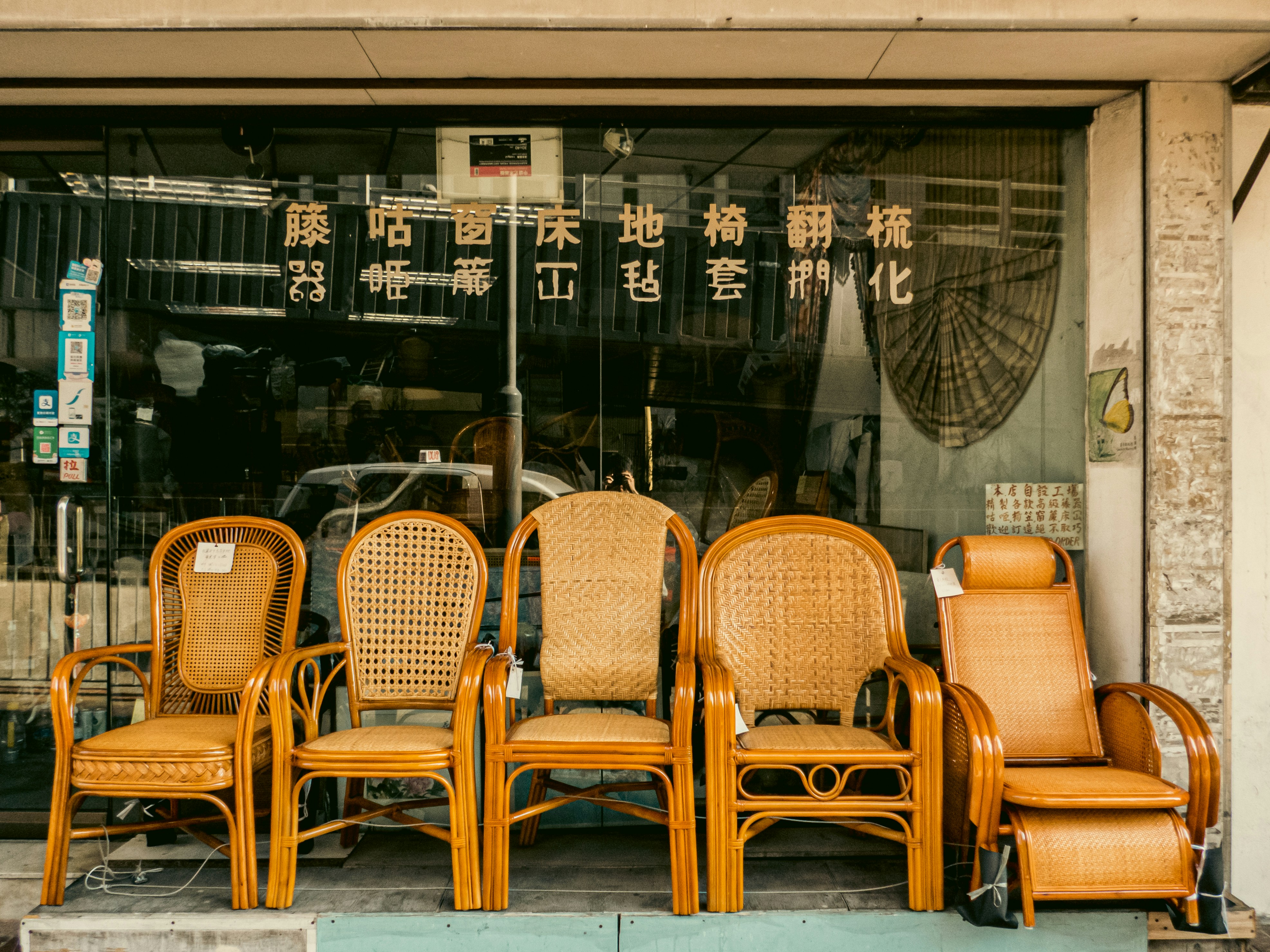 Rattan chairs lined outside a shop, their warm tones contrasting with glass windows reflecting urban life.