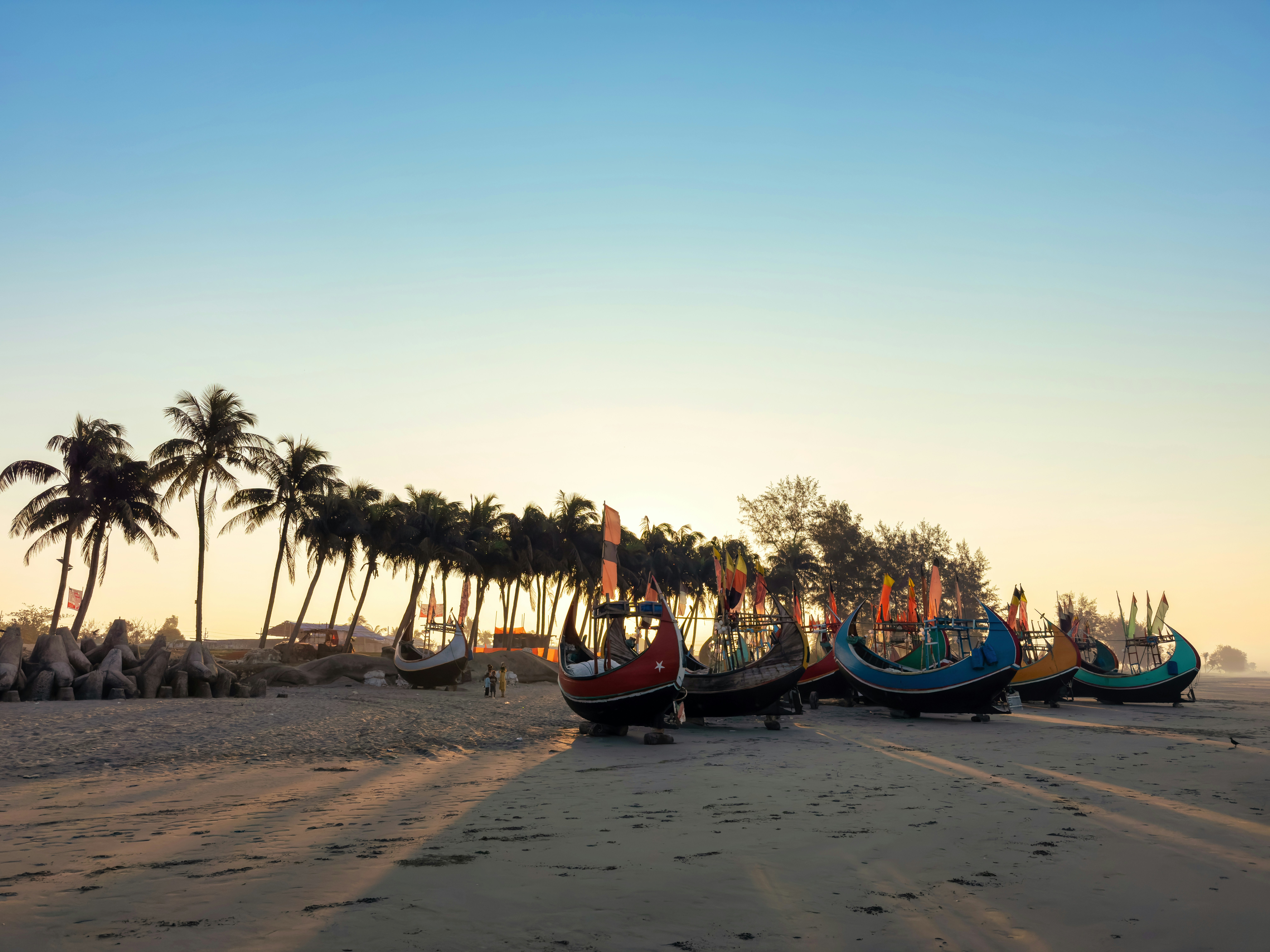 Colorful boats rest on sandy shore beneath silhouetted palms at dawn, with a soft gradient sky.