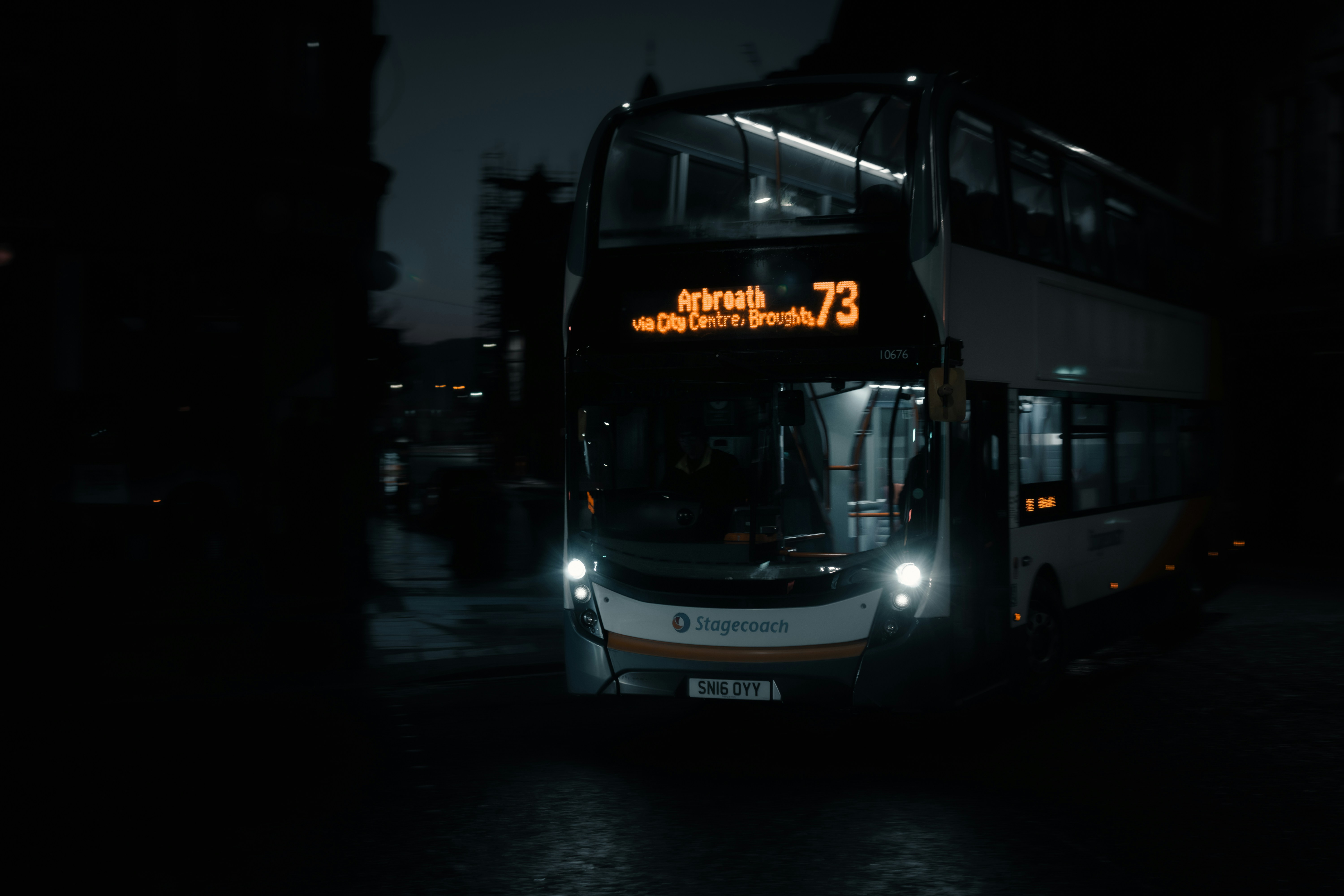 A double decker bus driving down a street at night photo – Free ...