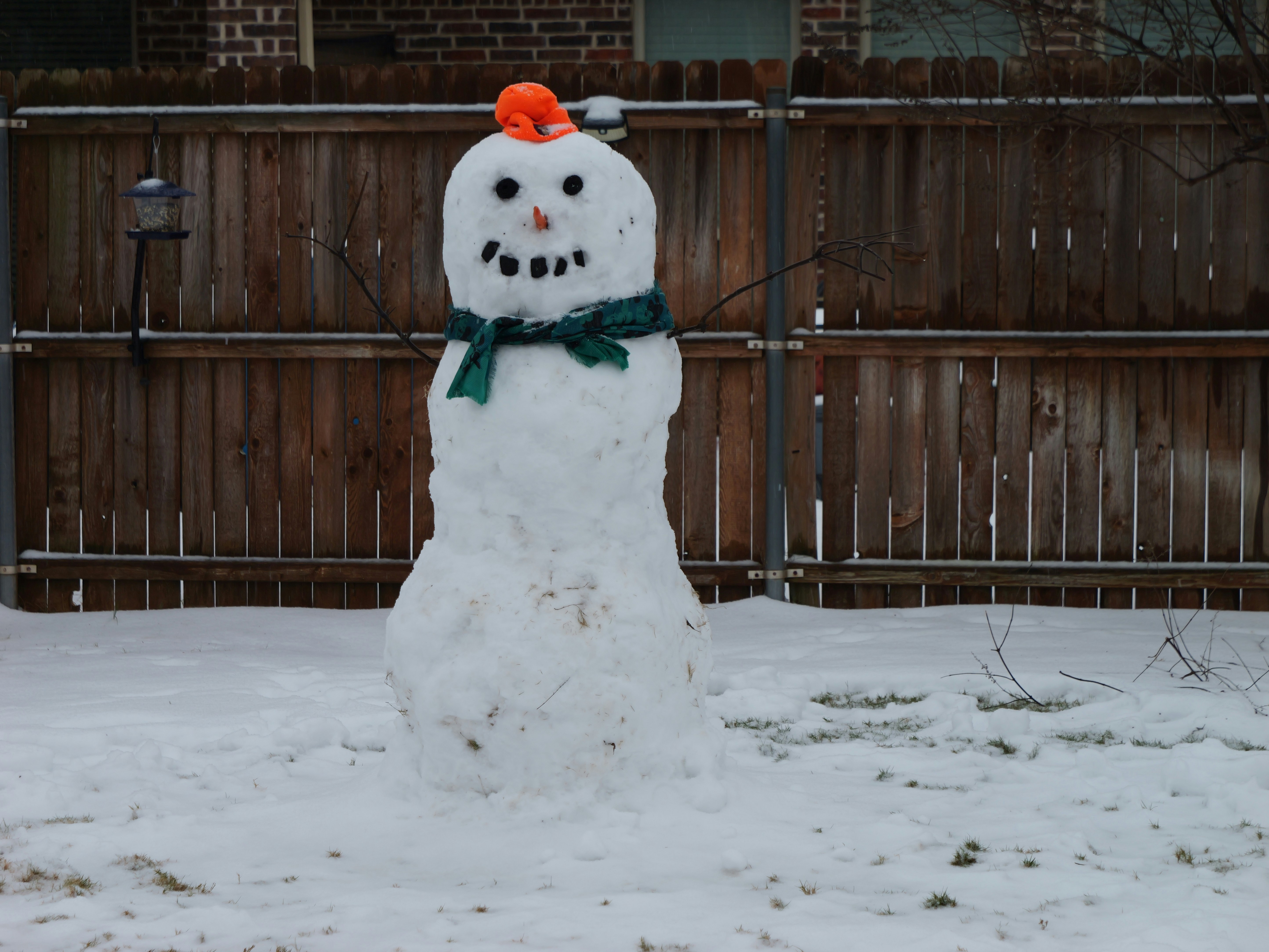 A snowman is standing in the snow in front of a fence photo – Free ...