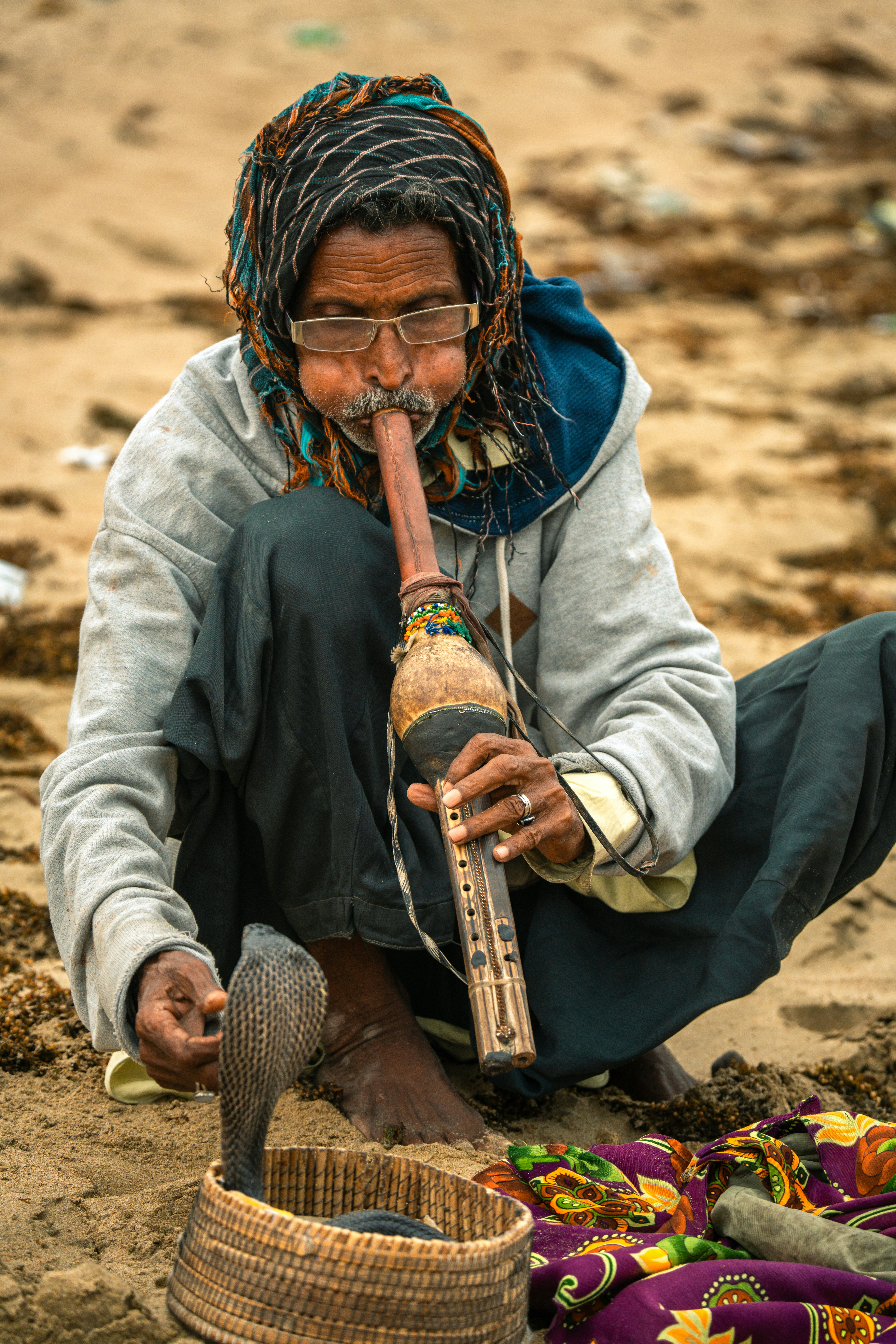 Desert Winds: A weathered musician breathes into a carved wind instrument amid sunlit sand.