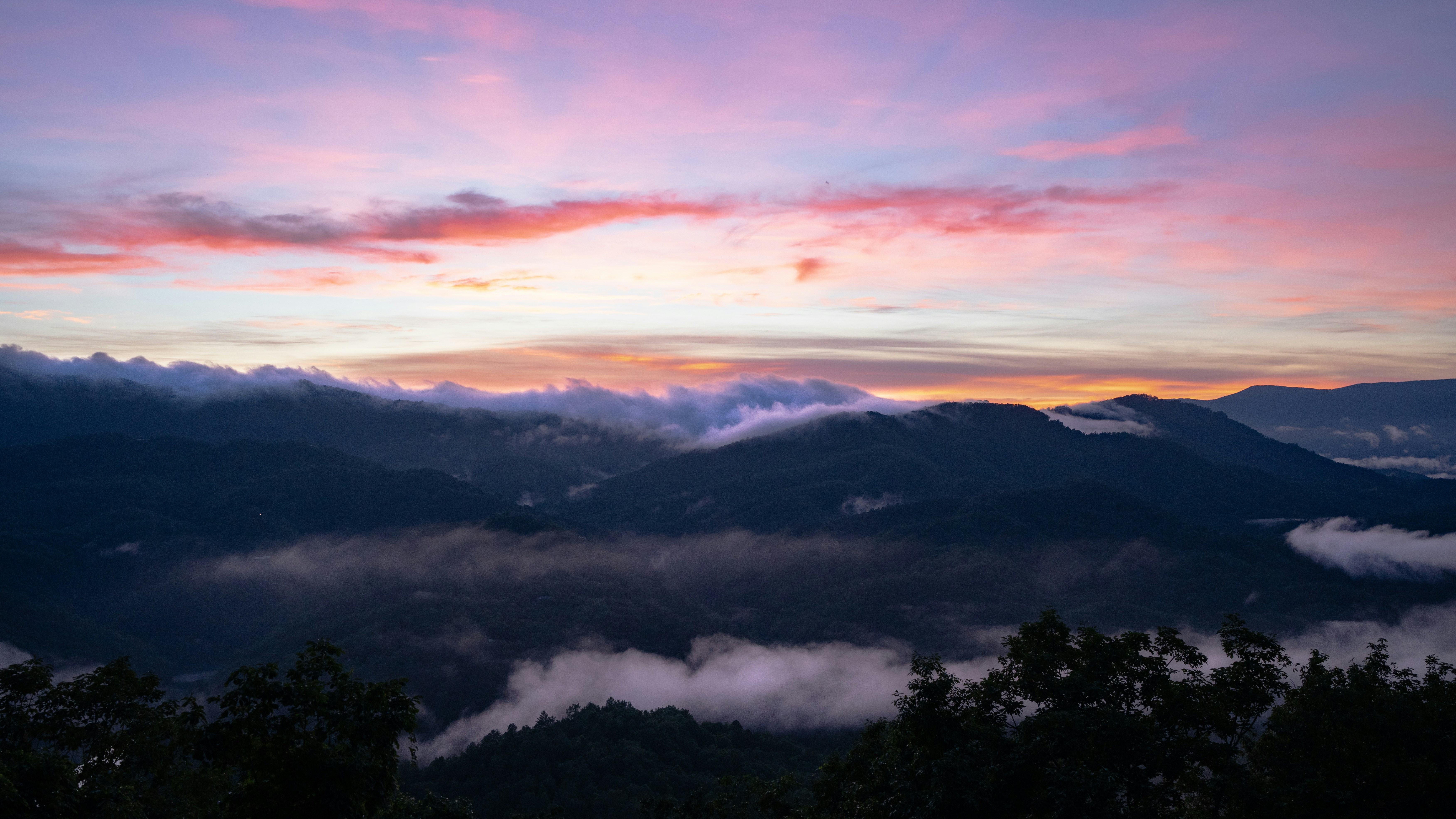 Sunrise colors blend over misty mountain ranges with silhouetted peaks.